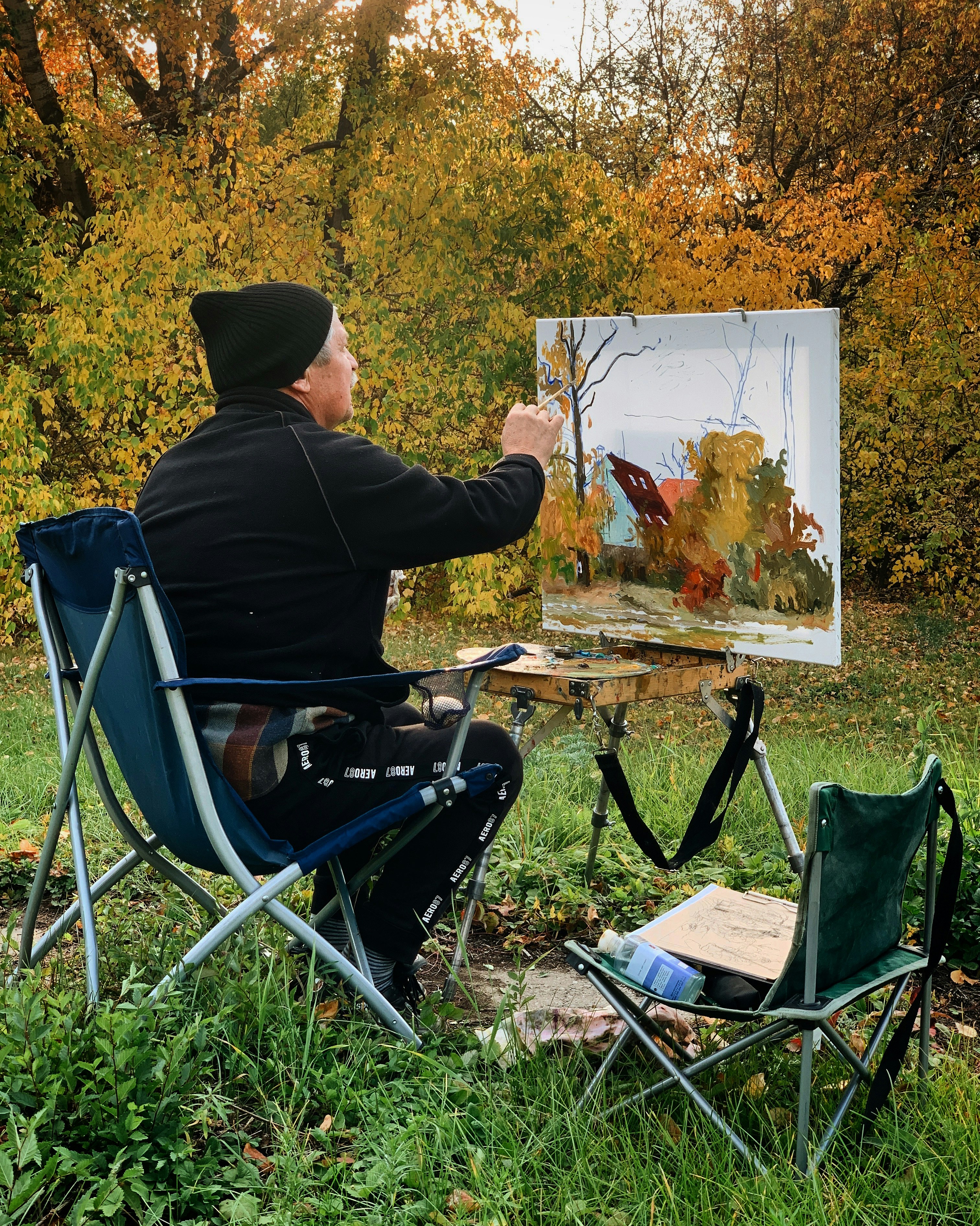 Artist capturing the vibrant colors of autumn foliage on canvas while seated outdoors. The scene showcases a serene connection between nature and creativity.