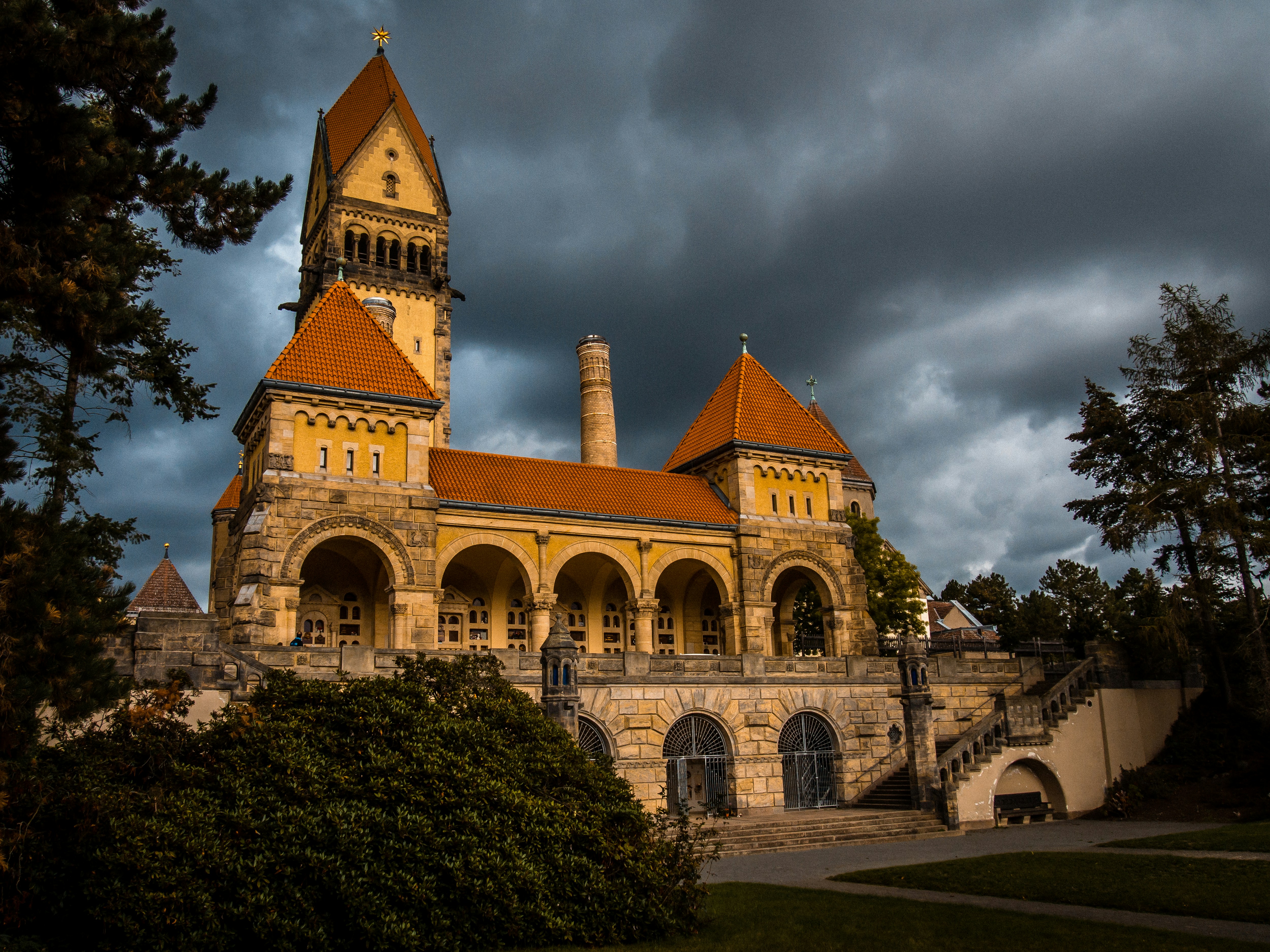 Historic building with red roofs and arches under a dramatic cloudy sky.
