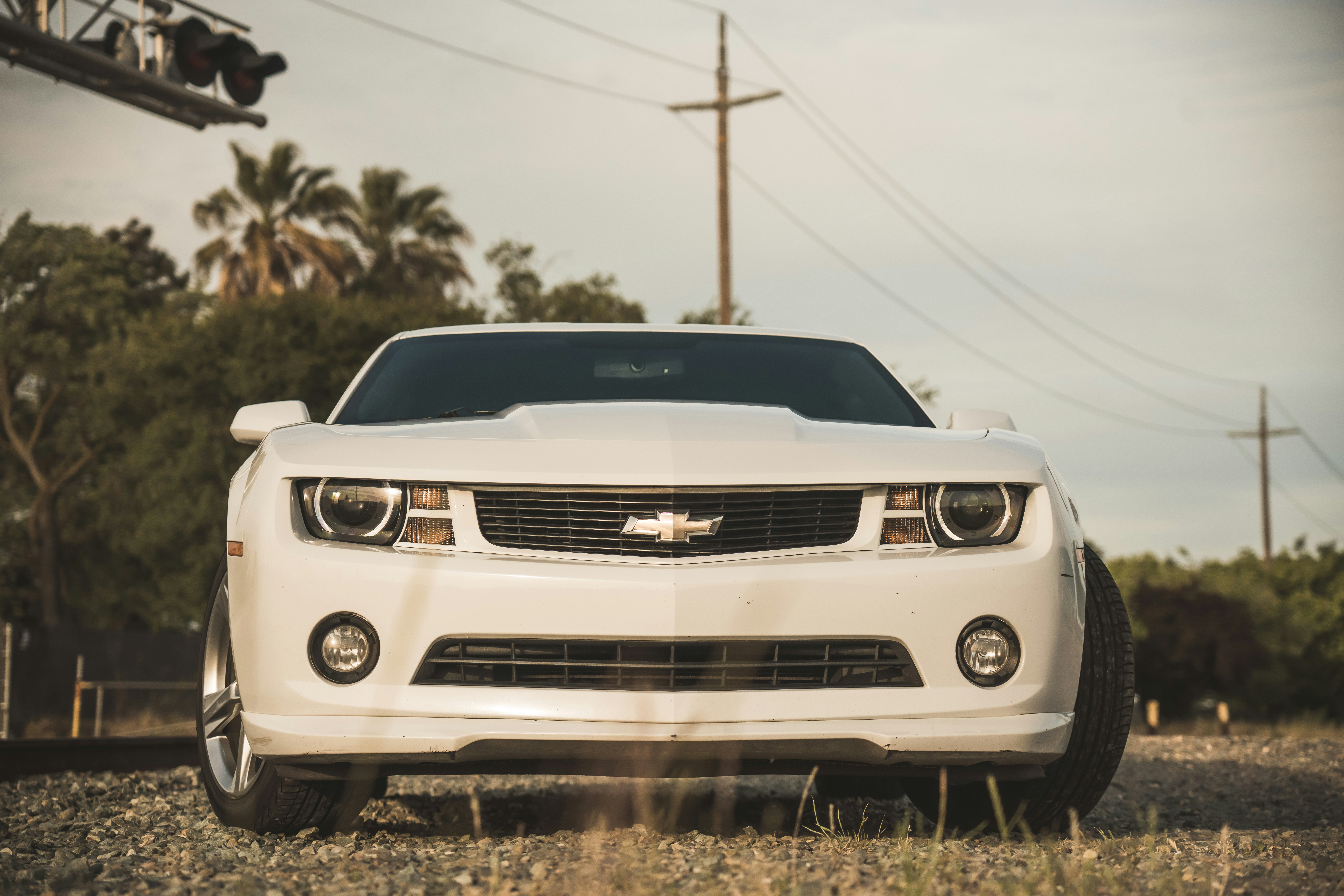 White Camaro SS parked on gravel with trees and power lines in the background.