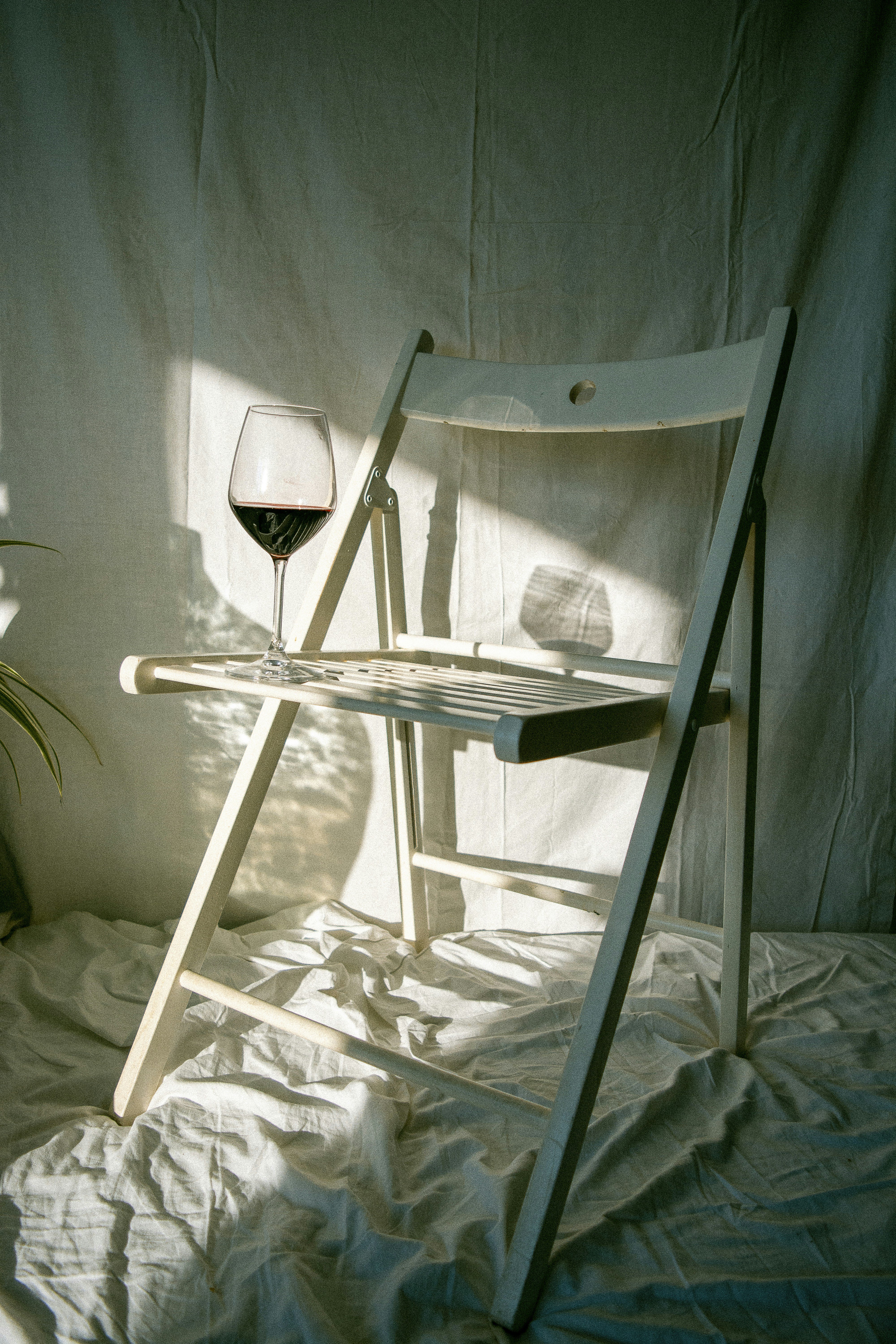 A white folding chair with a glass of red wine sits against a softly lit backdrop, capturing a serene moment of leisure.