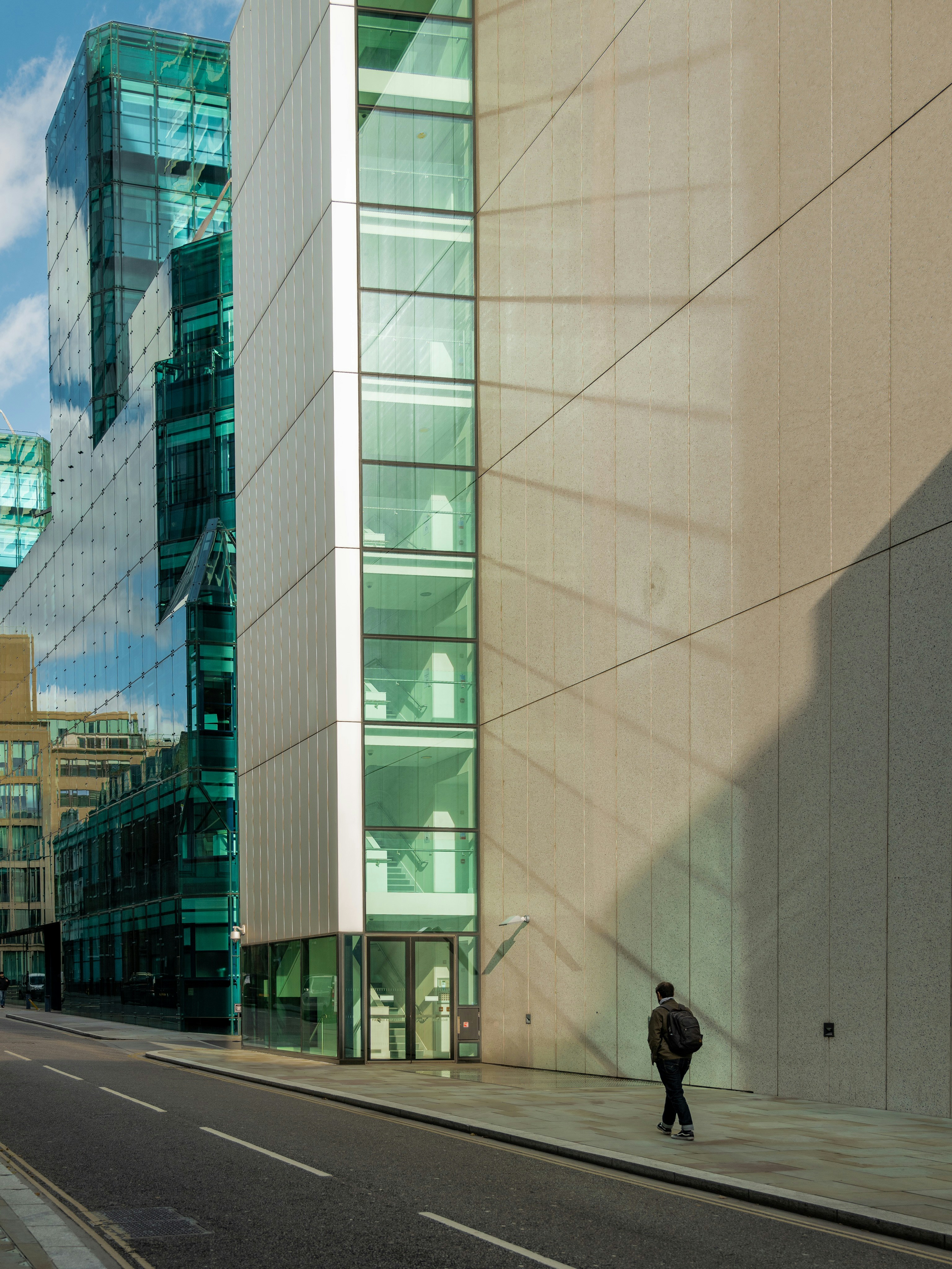 A lone figure walks along a modern street flanked by sleek glass and concrete architecture, showcasing the interplay of light and shadow.