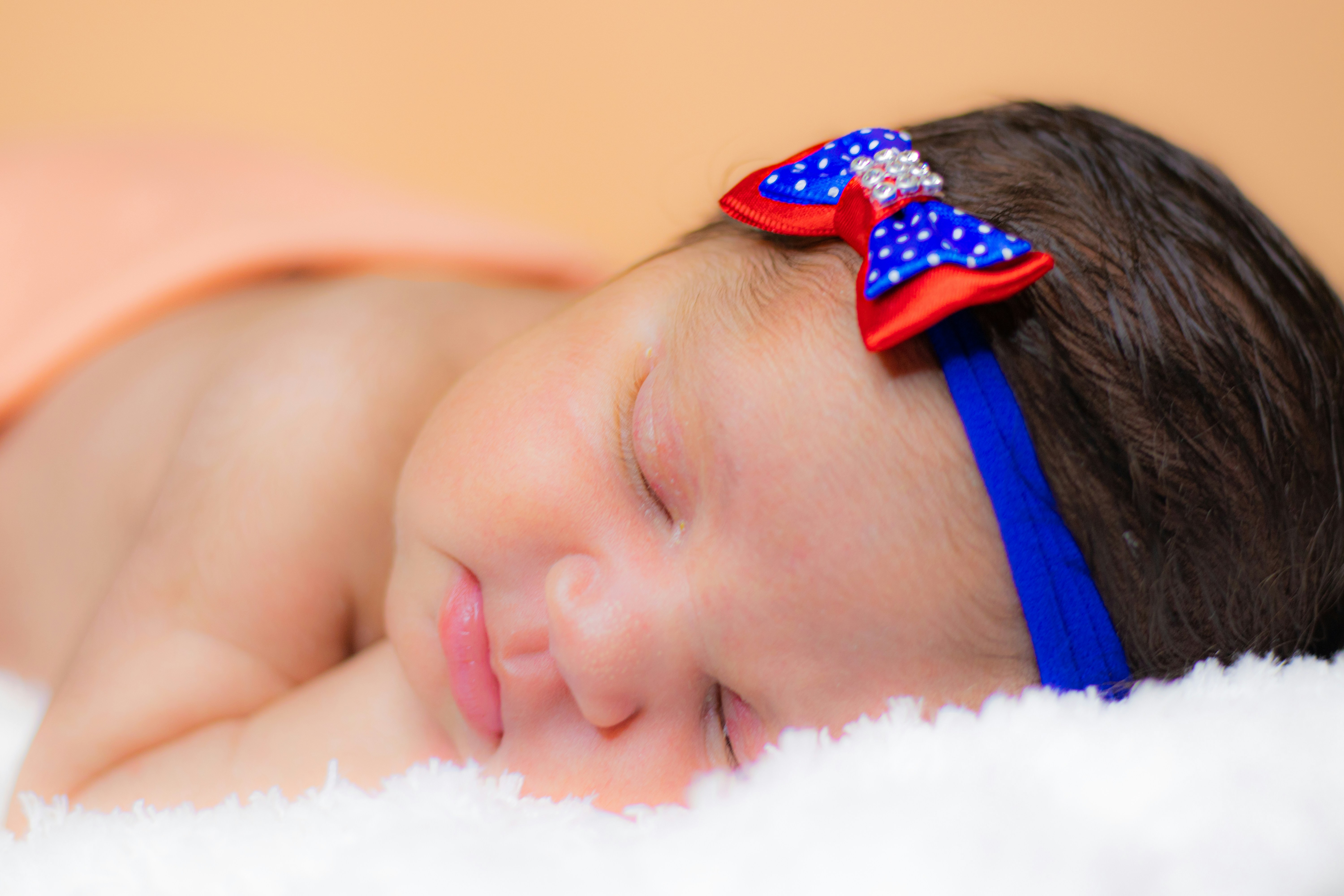 Sleeping newborn with patriotic bow resting on a soft white blanket