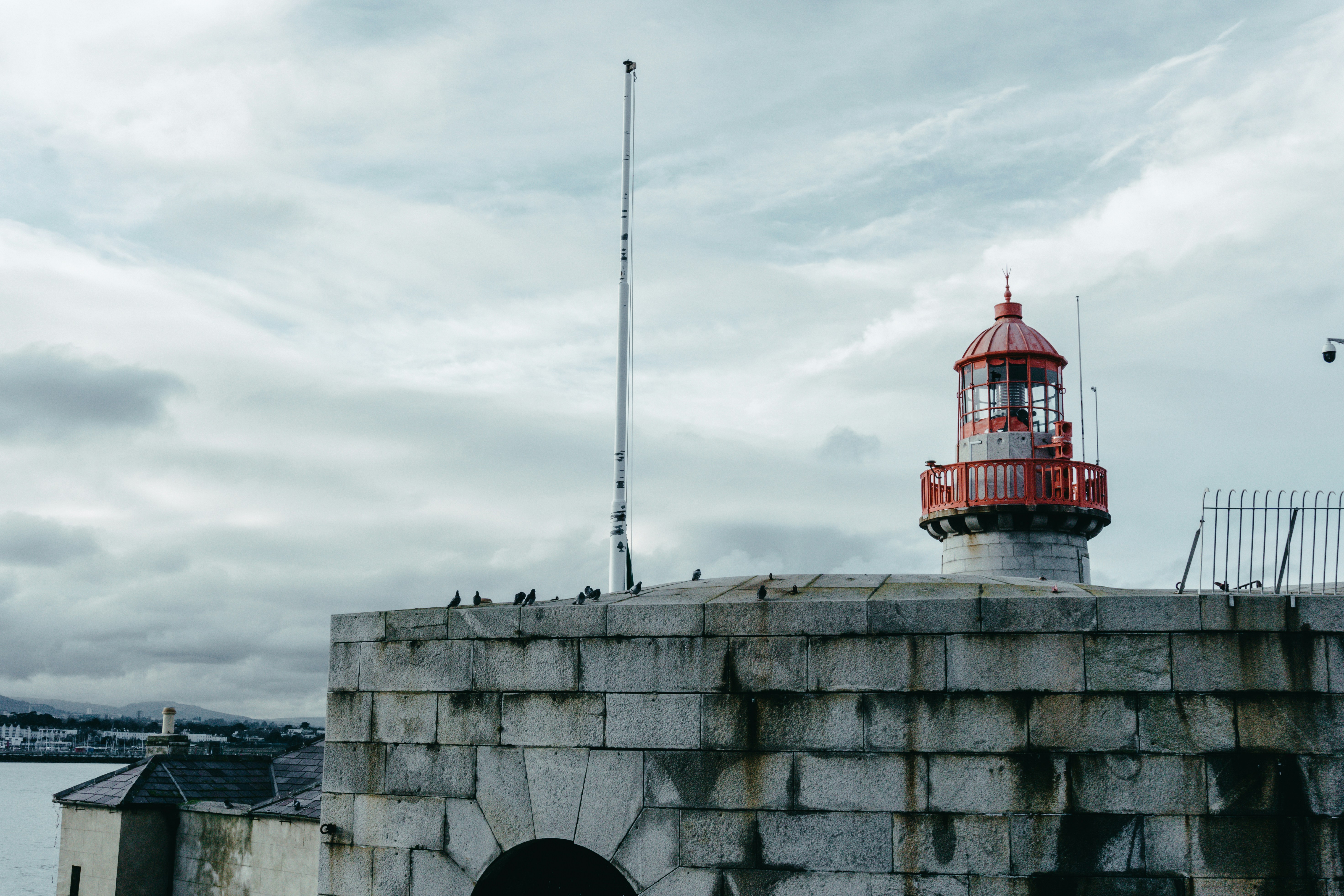 Red and white lighthouse perched on a stone structure beneath a cloudy sky.