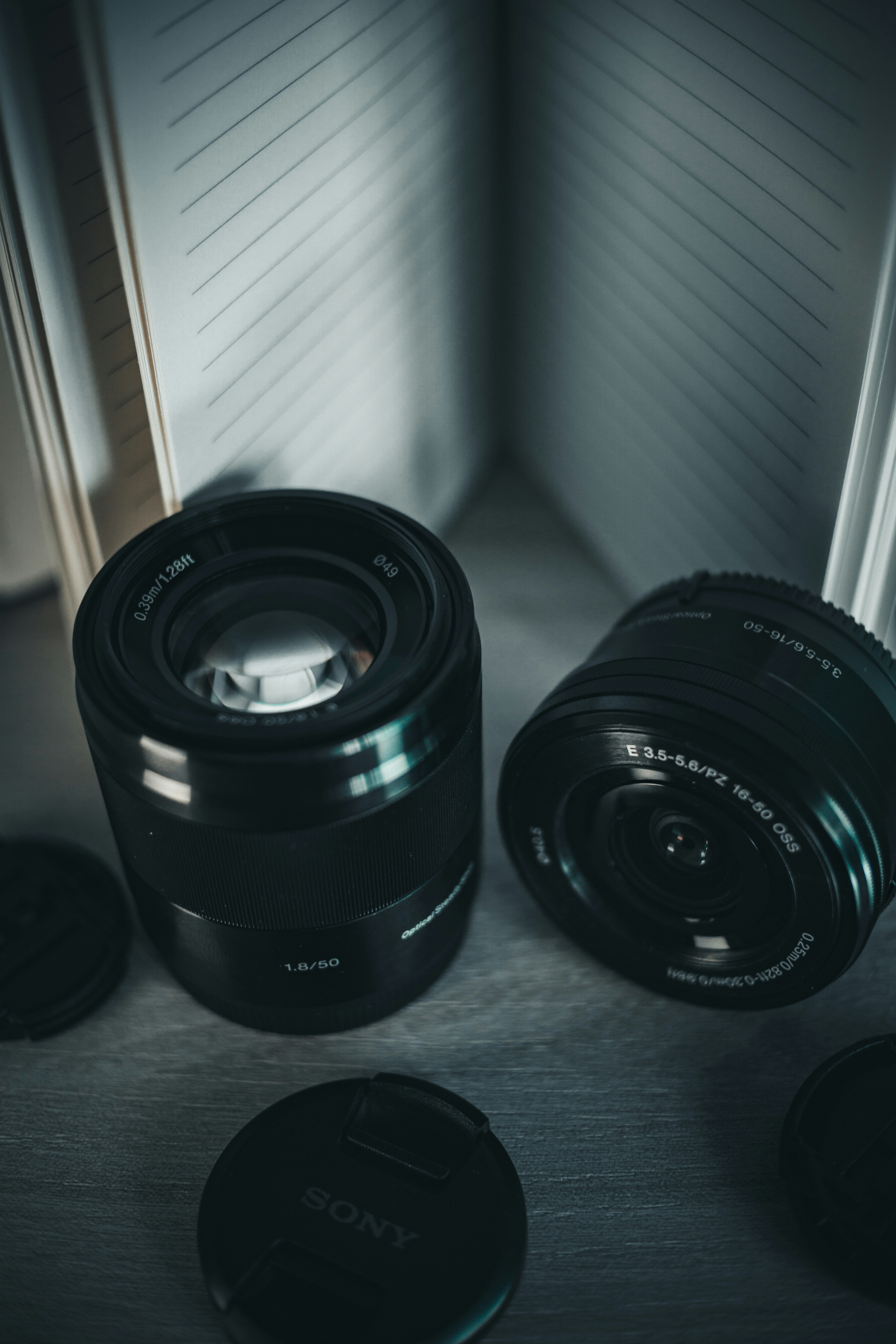 Two Sony camera lenses resting on a wooden surface, surrounded by an open notebook. The sleek design highlights the tools of a photographer's craft.