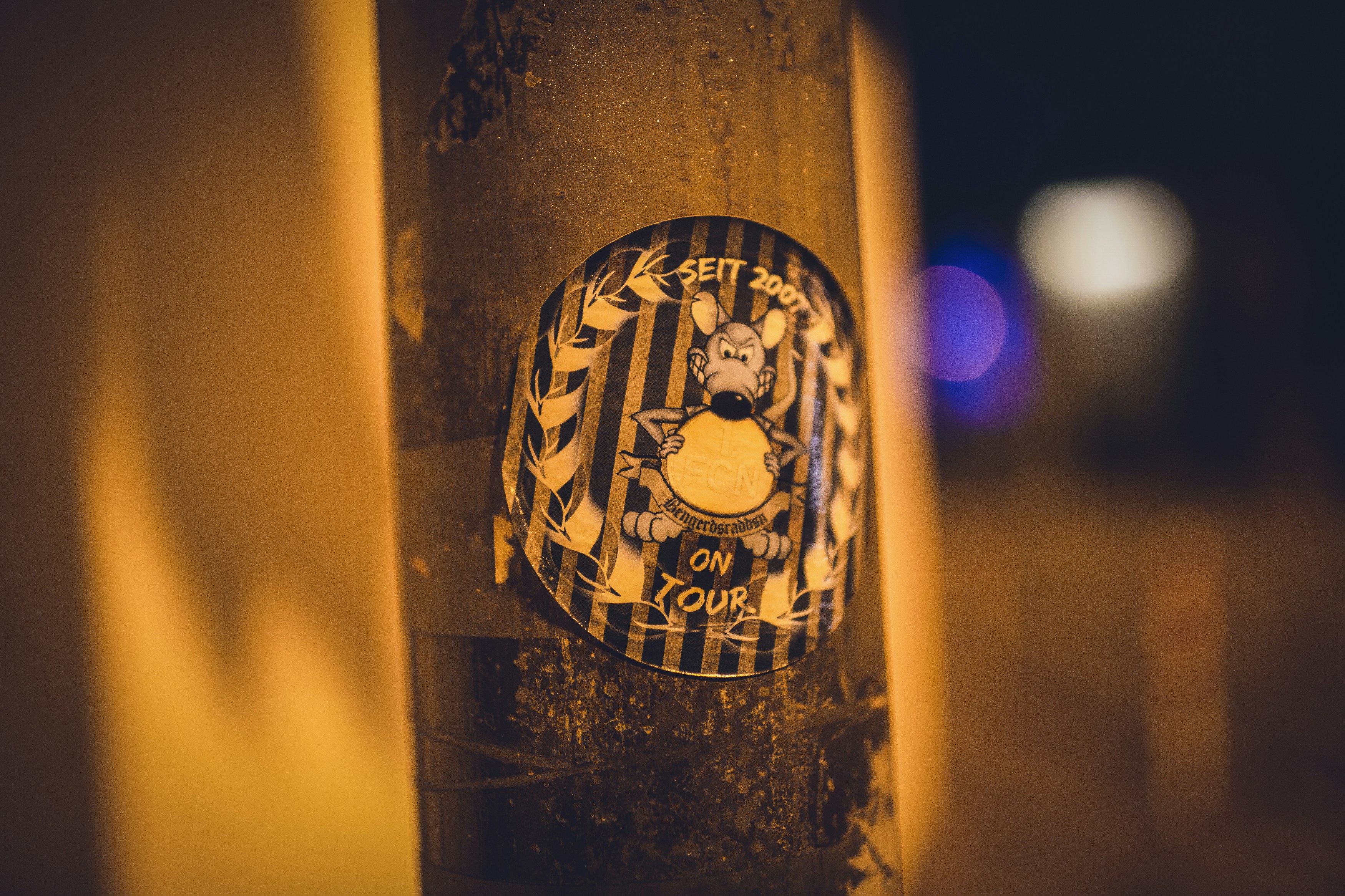 Bear-on-Tour Badge on a Weathered Street Pole in Amber Night Glow