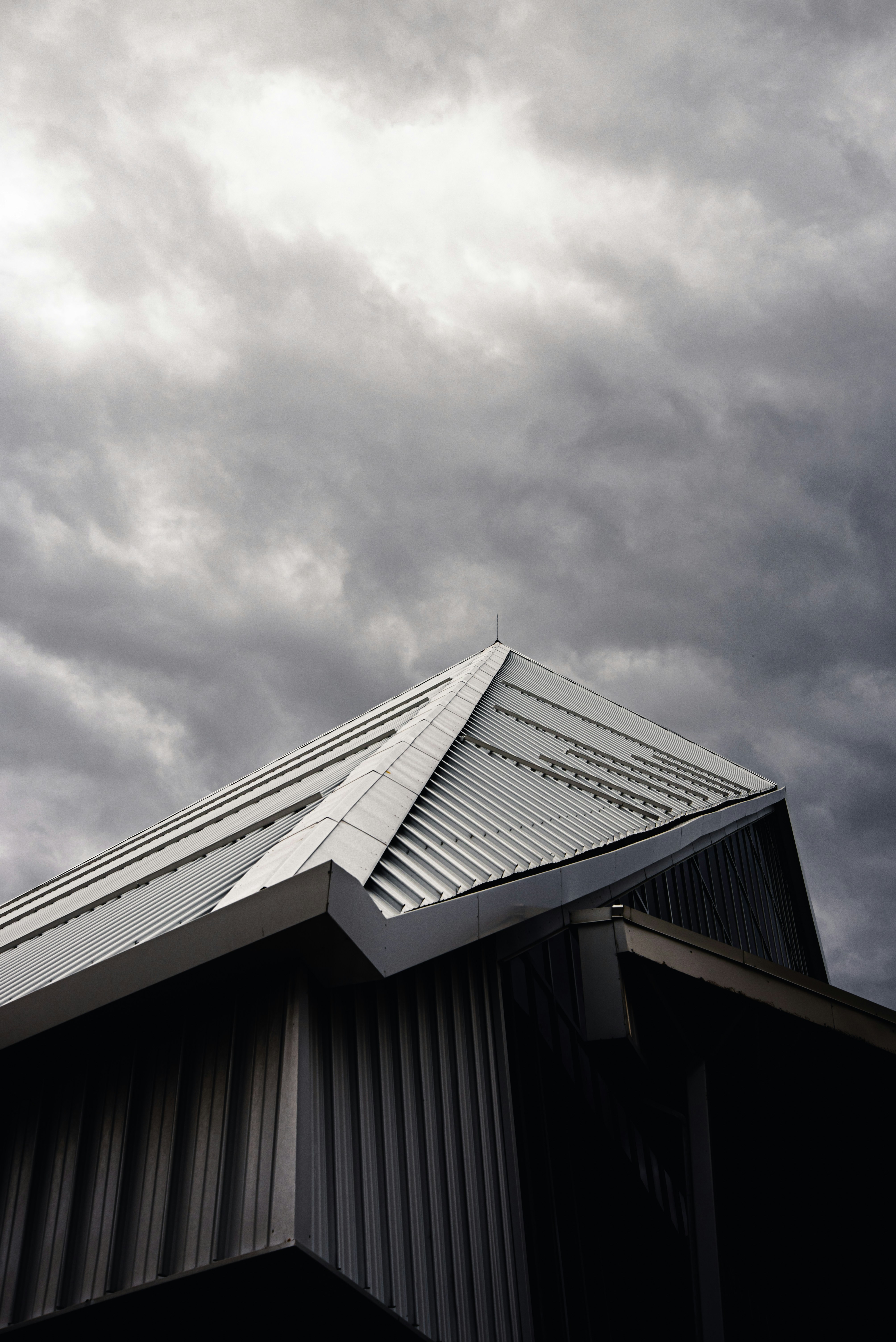Angular metal roof of a contemporary building under a dramatic sky filled with clouds.