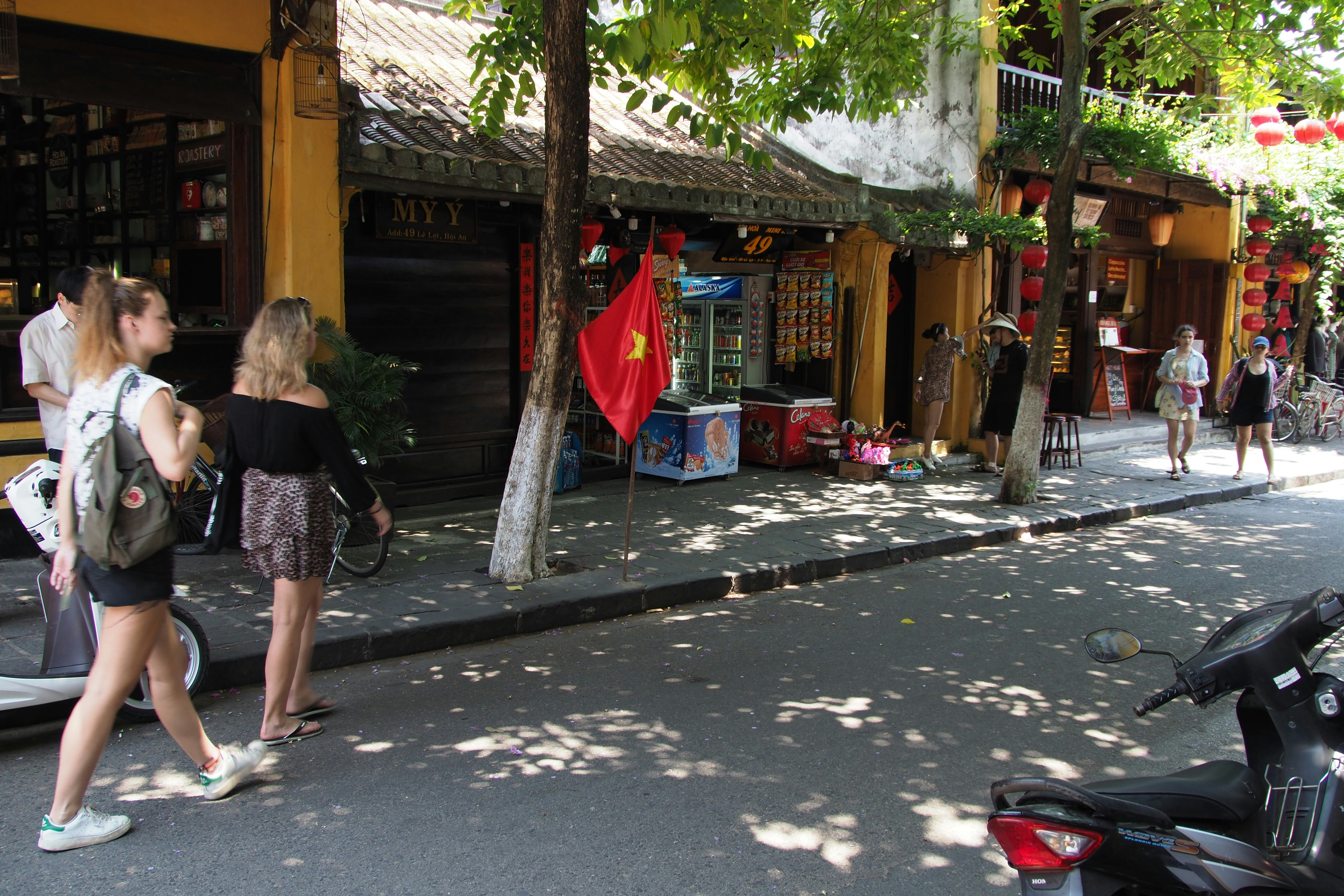 Vietnamese Street Scene bathed in dappled shade with a red flag fluttering