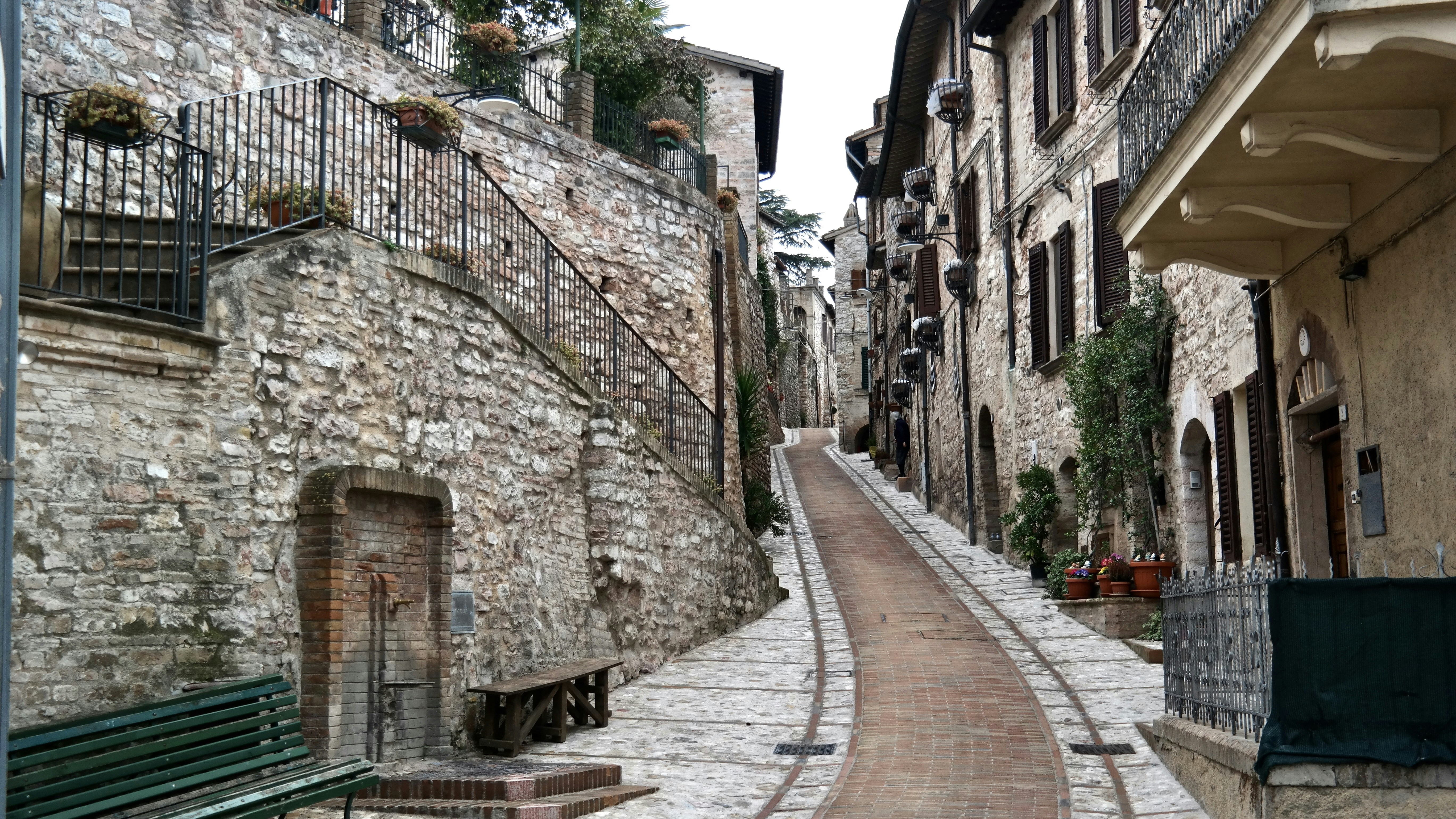 Narrow cobblestone street winding between aged stone buildings in a quaint village setting.