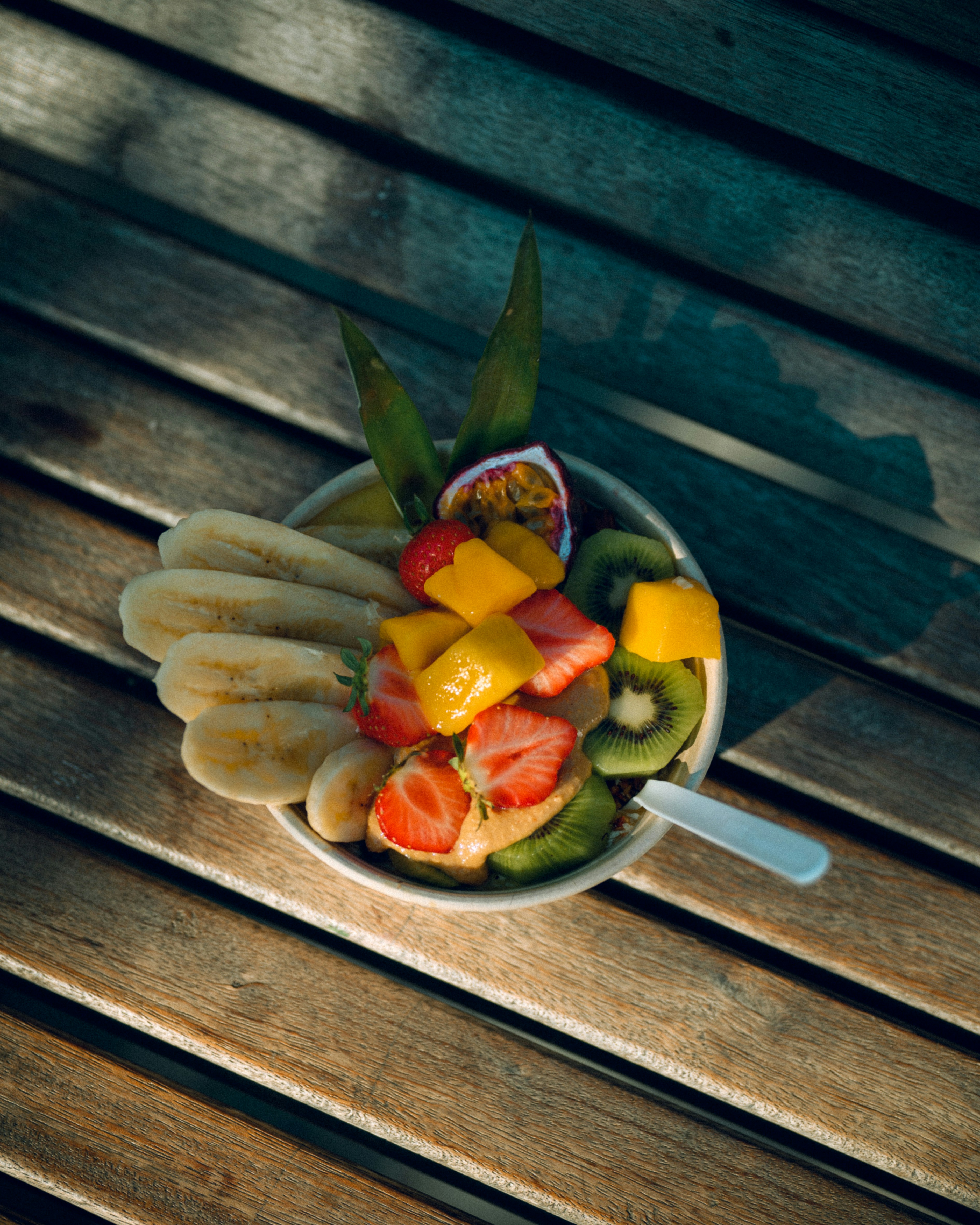 A vibrant assortment of fresh fruits including bananas, strawberries, kiwi, and mango, arranged artfully in a bowl against a wooden backdrop.