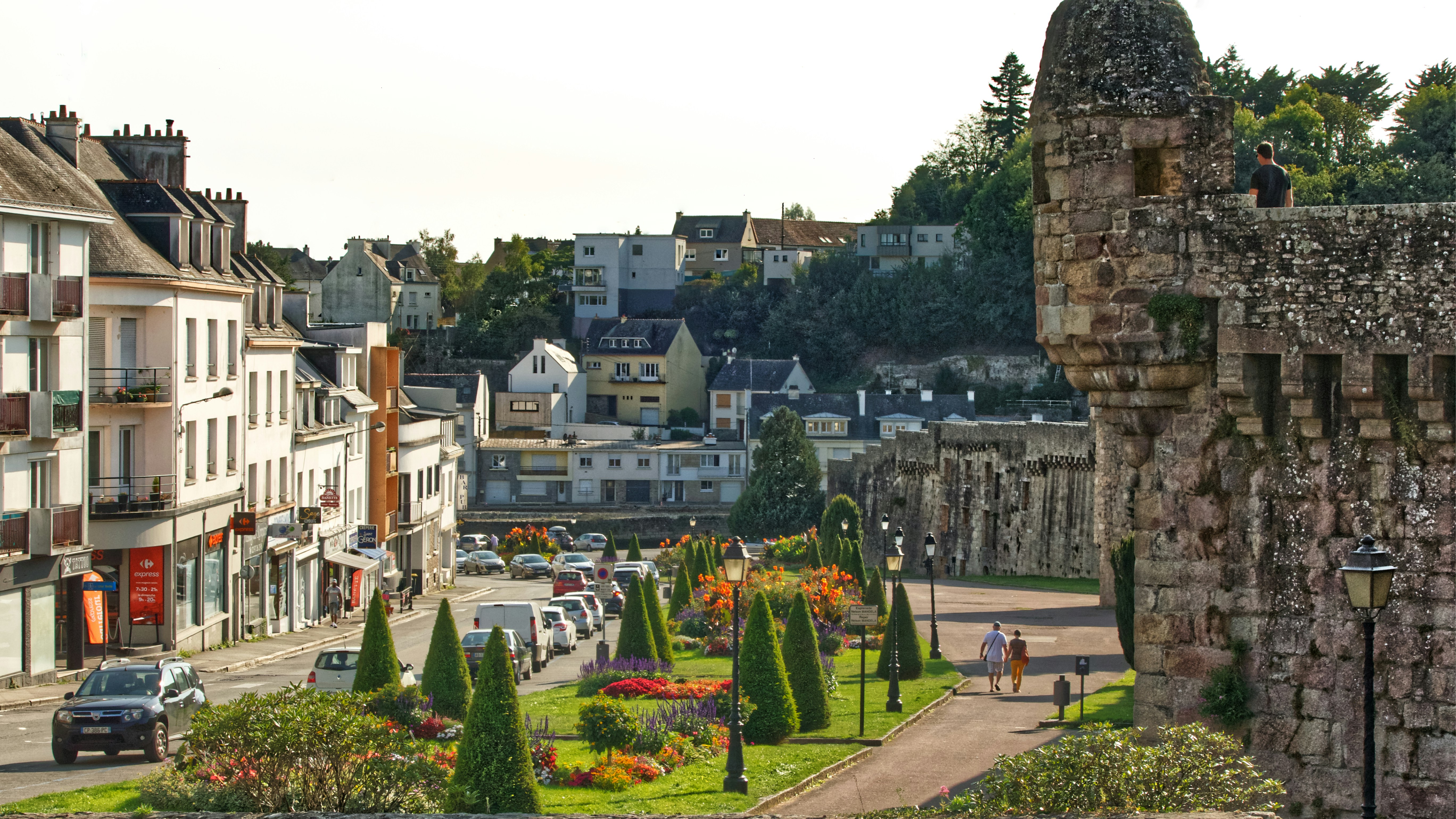 Rampart Overlook: A Sunlit Town Street Framed by Historic Walls and Pruned Gardens