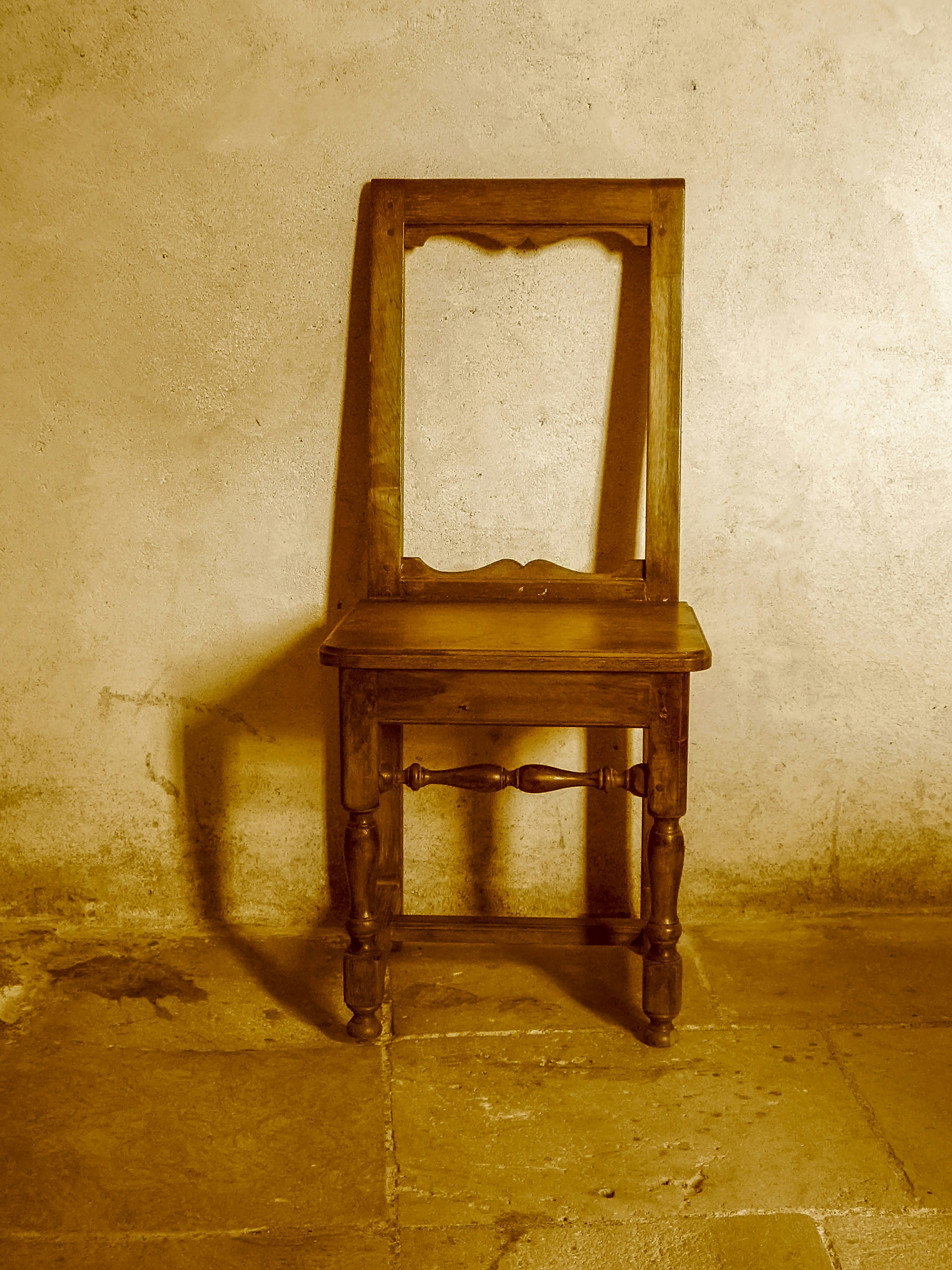 An empty wooden chair with a missing backrest set against a textured wall, evoking feelings of nostalgia and absence.