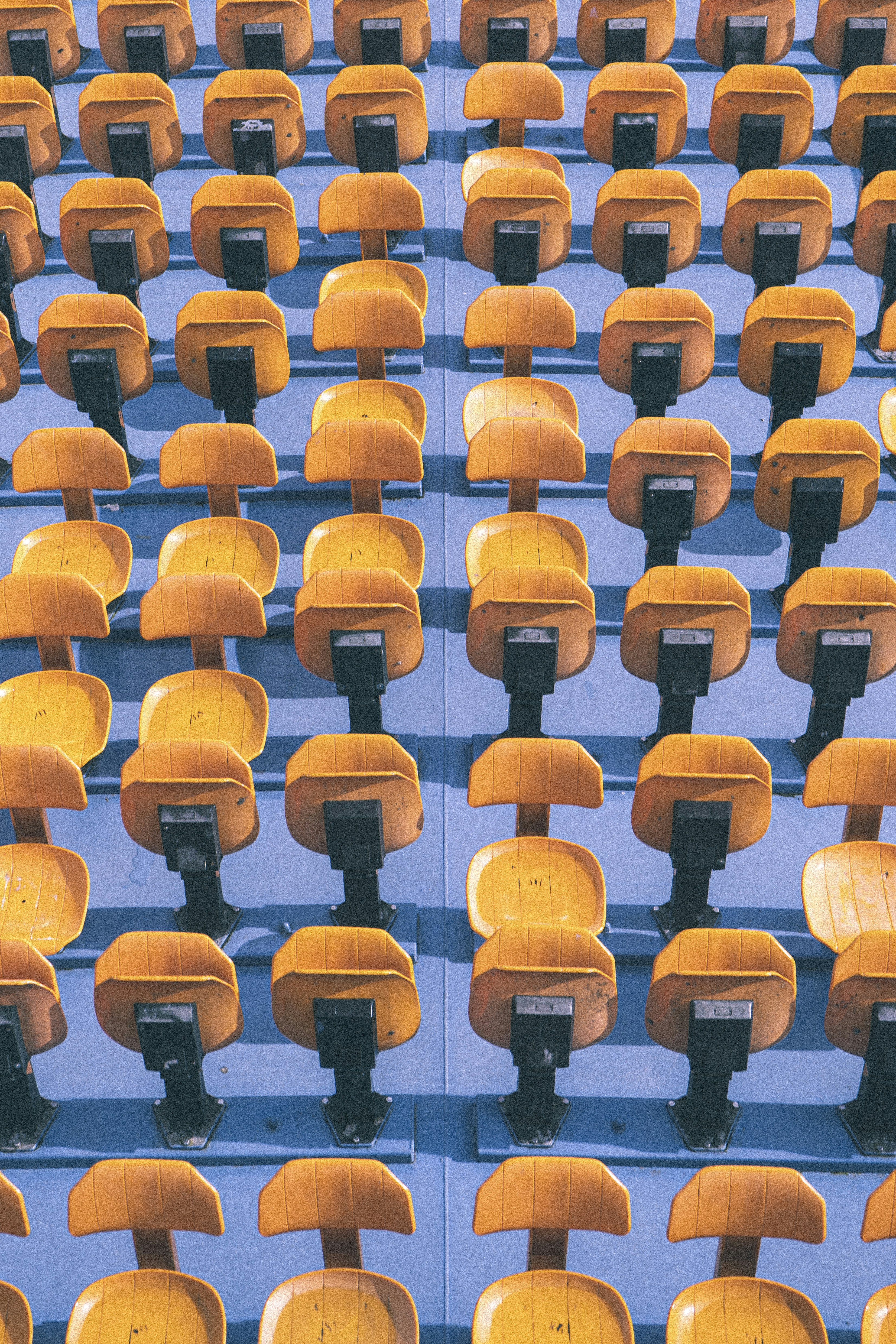An abstract arrangement of yellow stadium seats against a blue backdrop, showcasing a geometric pattern and inviting contemplation on space and design.