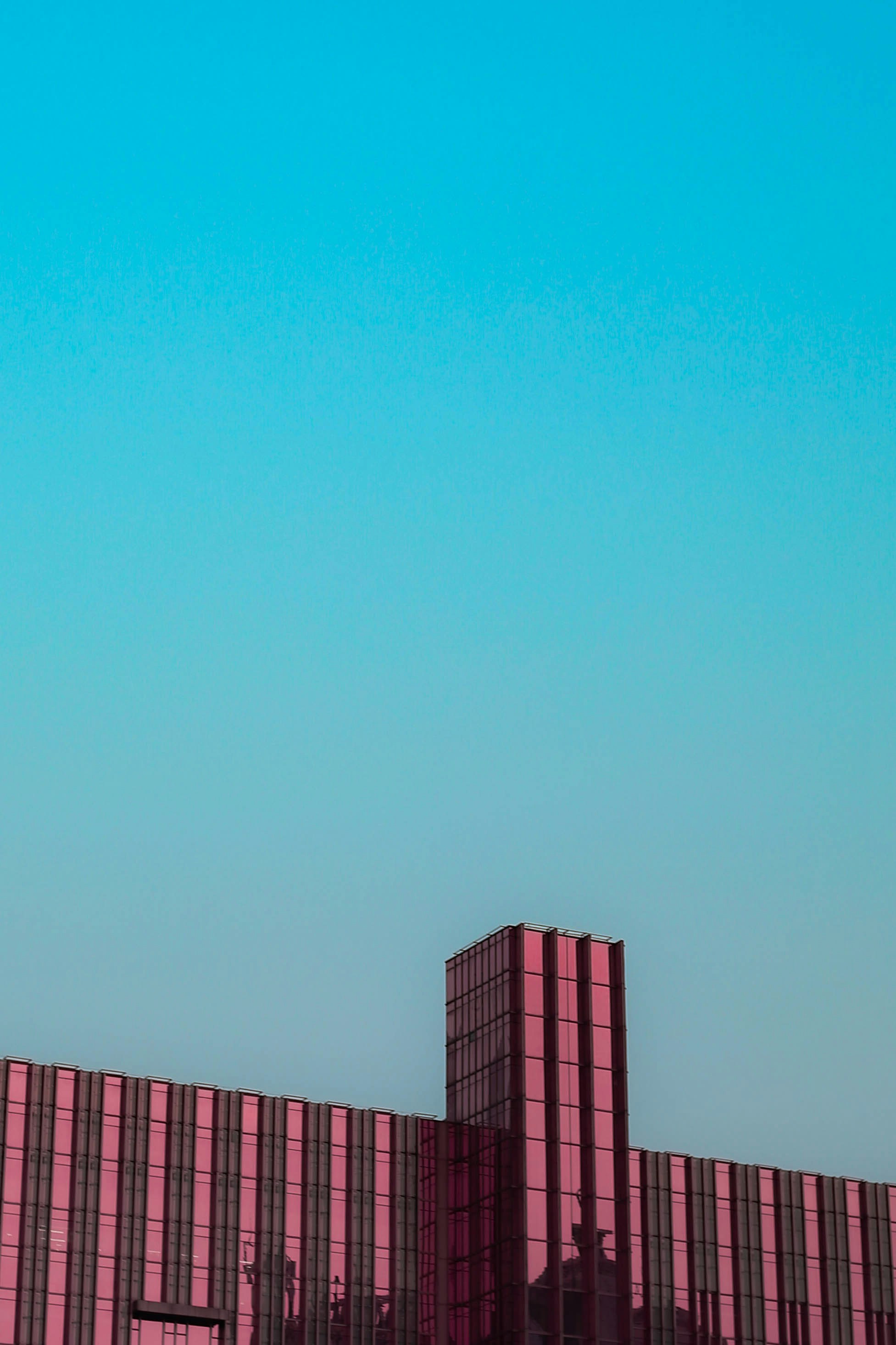 Contemporary building with striking pink glass facade reflecting a clear blue sky.