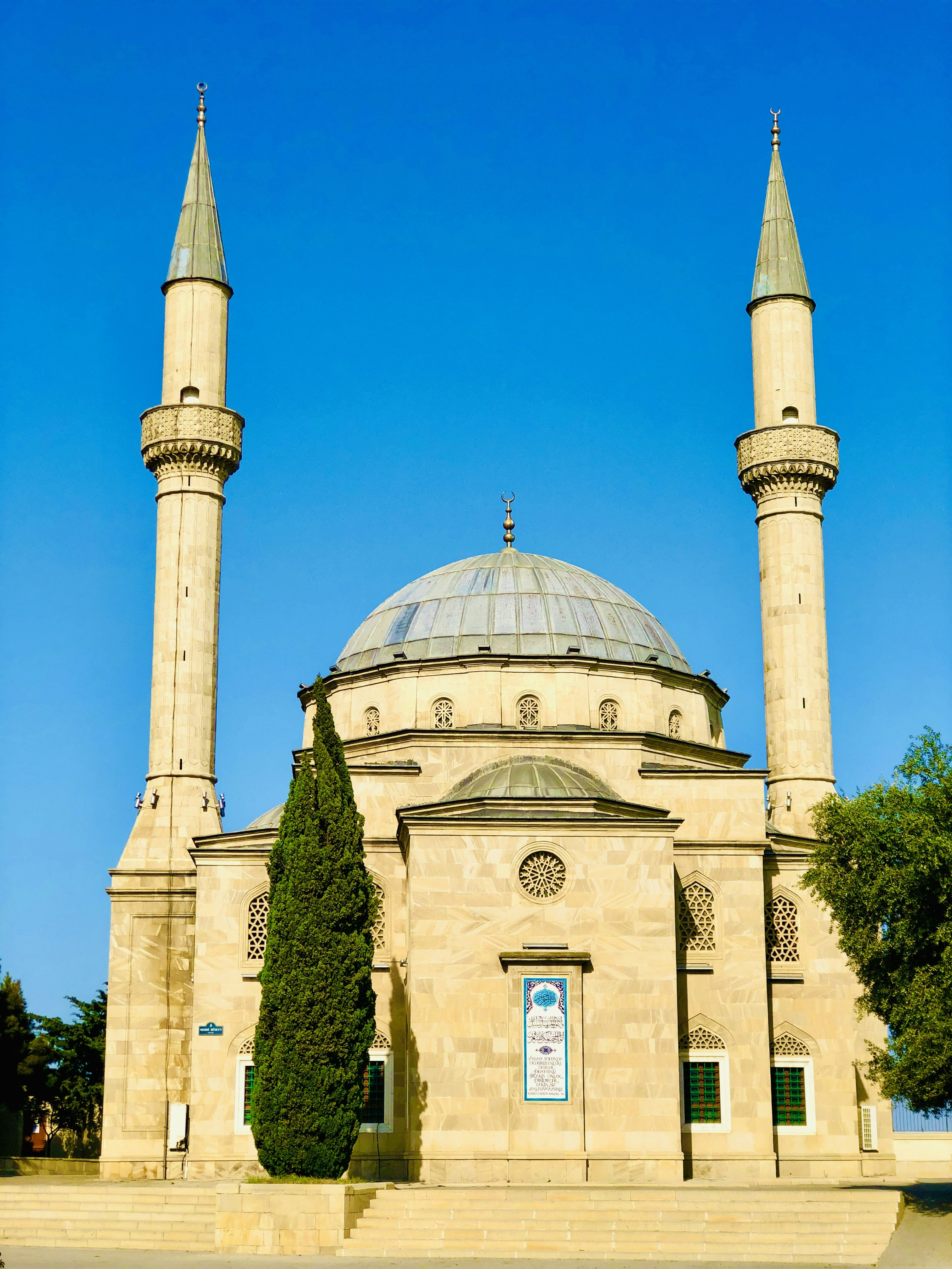 Historic mosque featuring elegant minarets and a domed roof against a clear blue sky.
