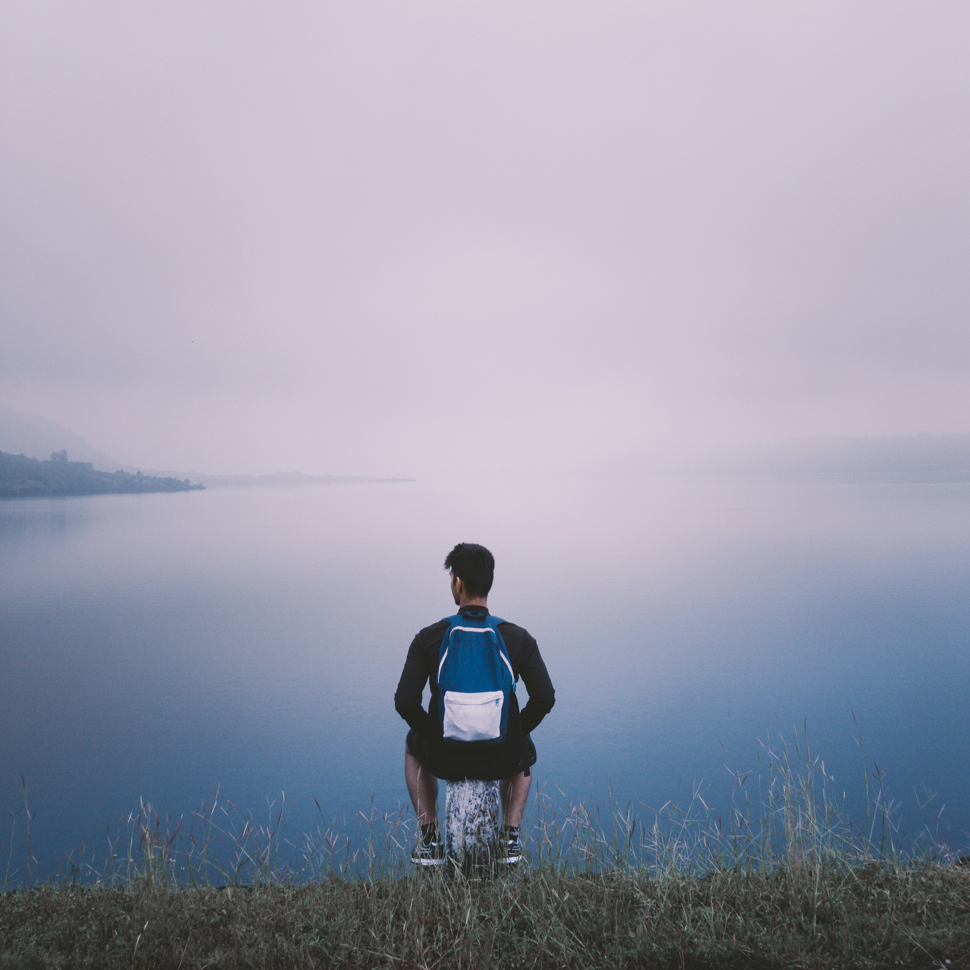 Man in blue and black shirt standing on green grass field near body of ...