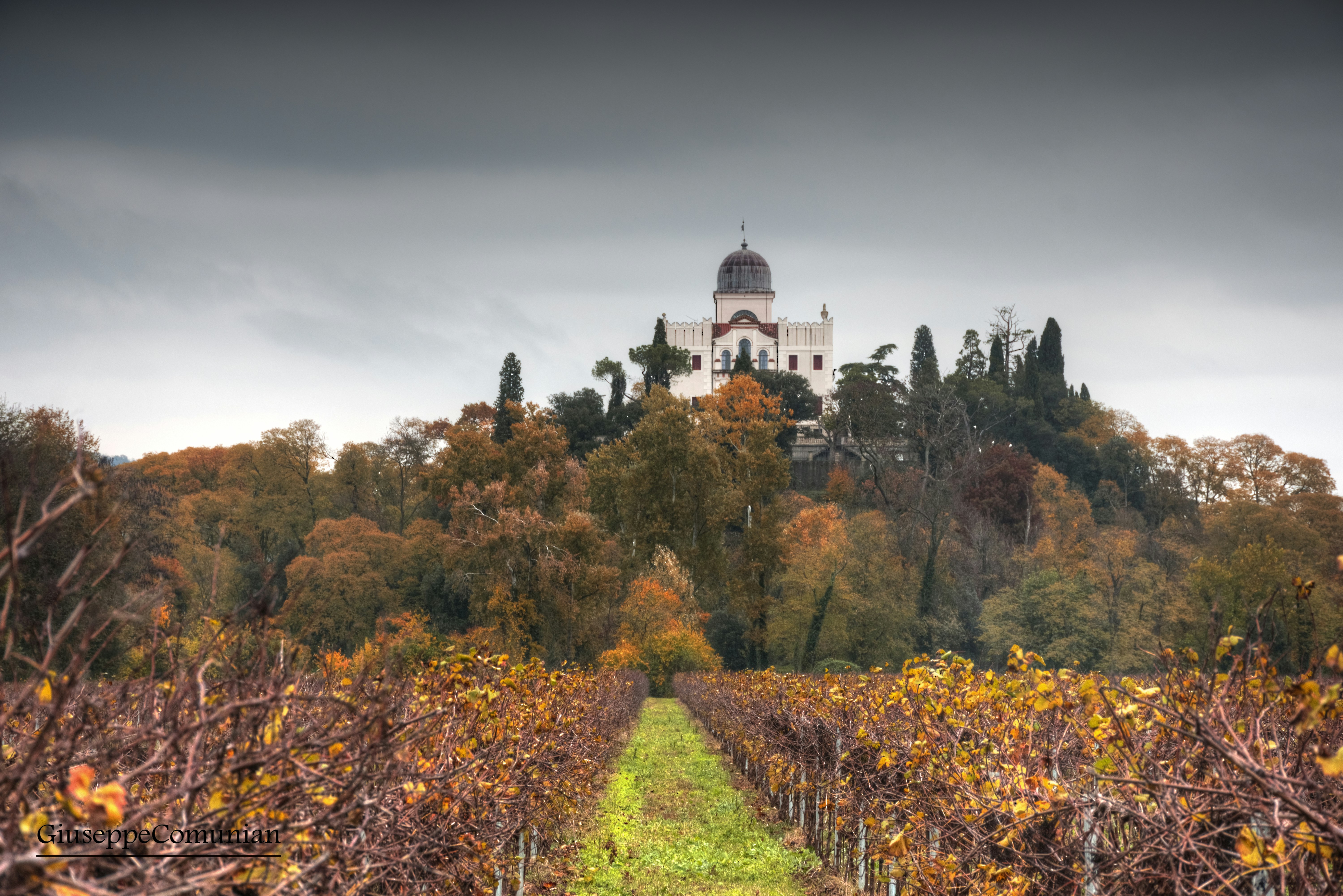 Church perched on a wooded hill, framed by vibrant autumn foliage under a moody sky.