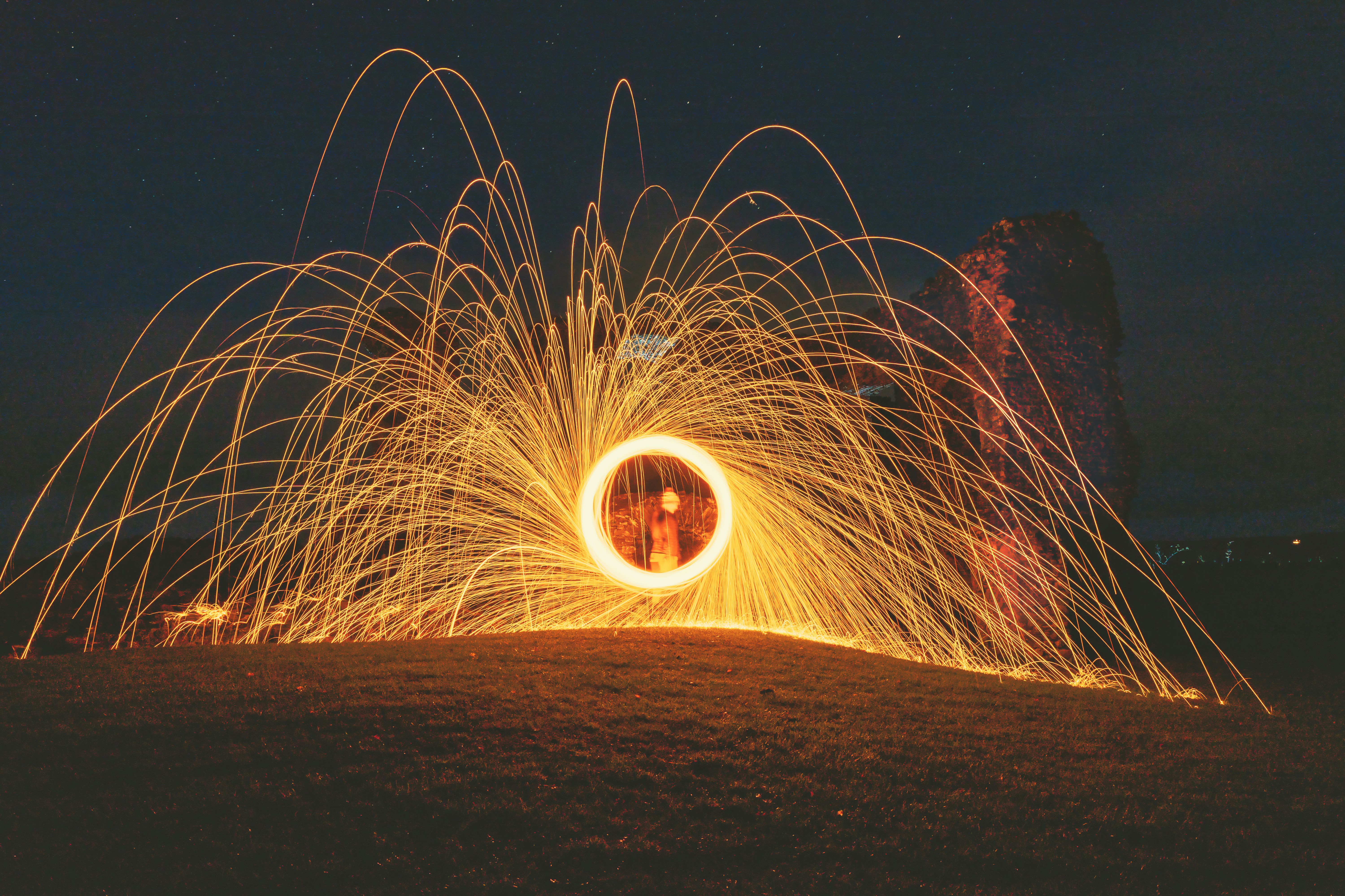A mesmerizing display of steel wool spinning, creating vibrant trails of light against a dark night sky. The circular glow frames the scene, enhancing the dynamic motion.