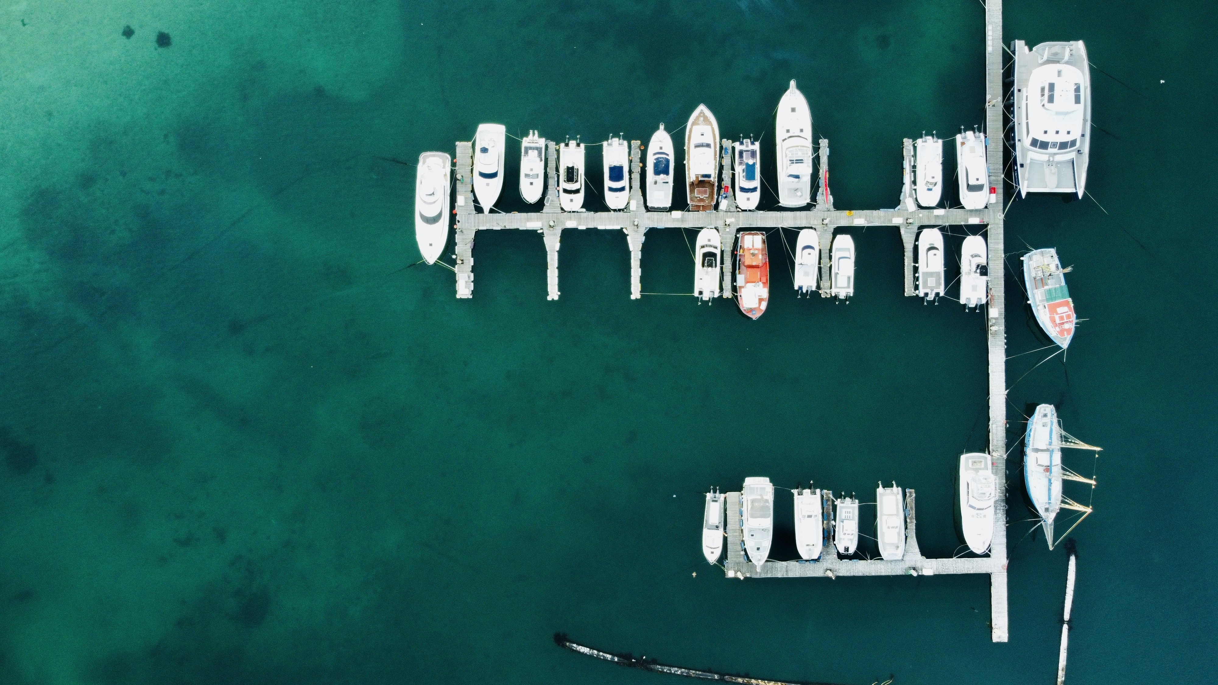 Aerial perspective of boats moored at a dock on tranquil turquoise water.