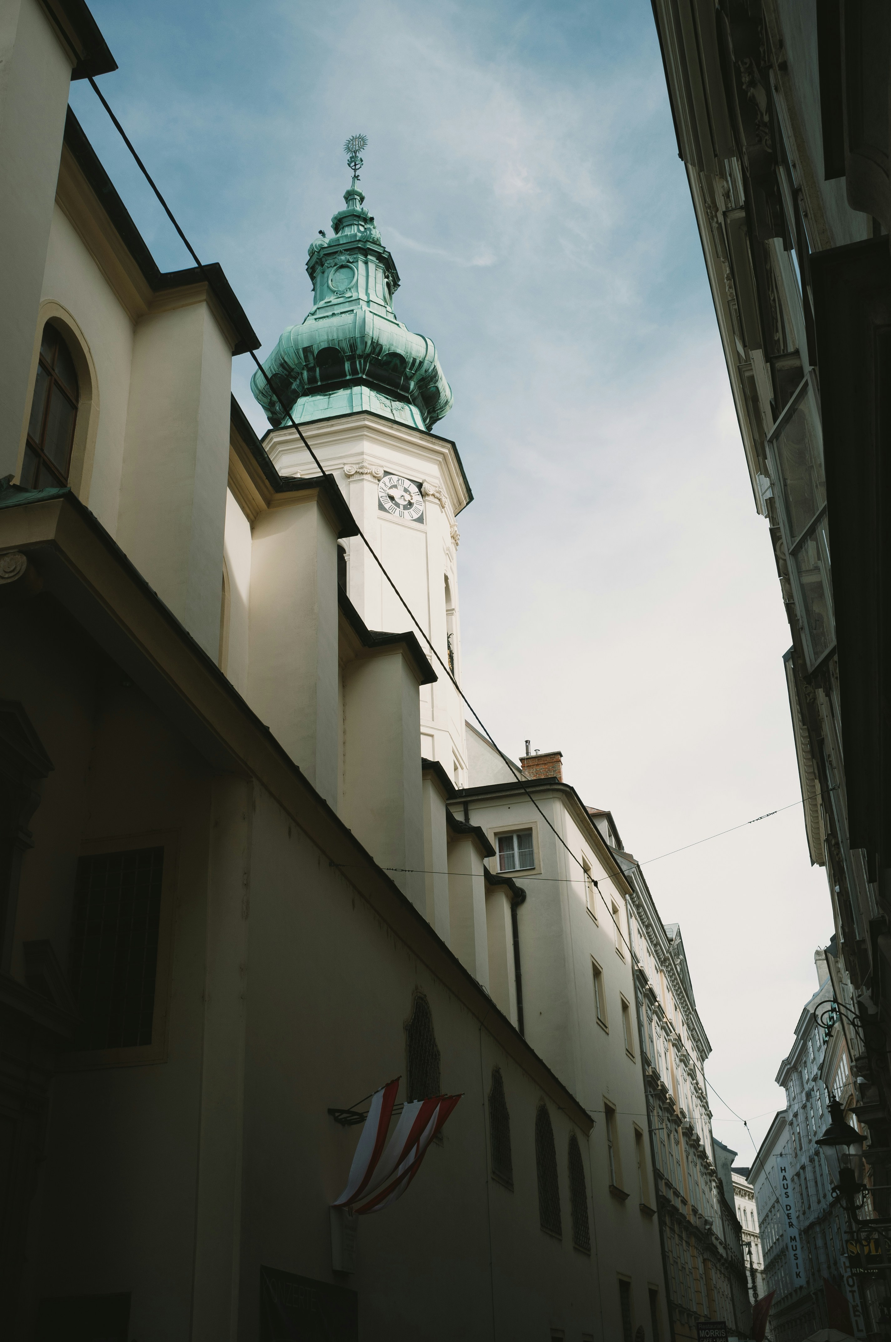 Historic building with a green dome towering above a narrow alleyway, framed by old architecture. Austrian flag flutters gently below.