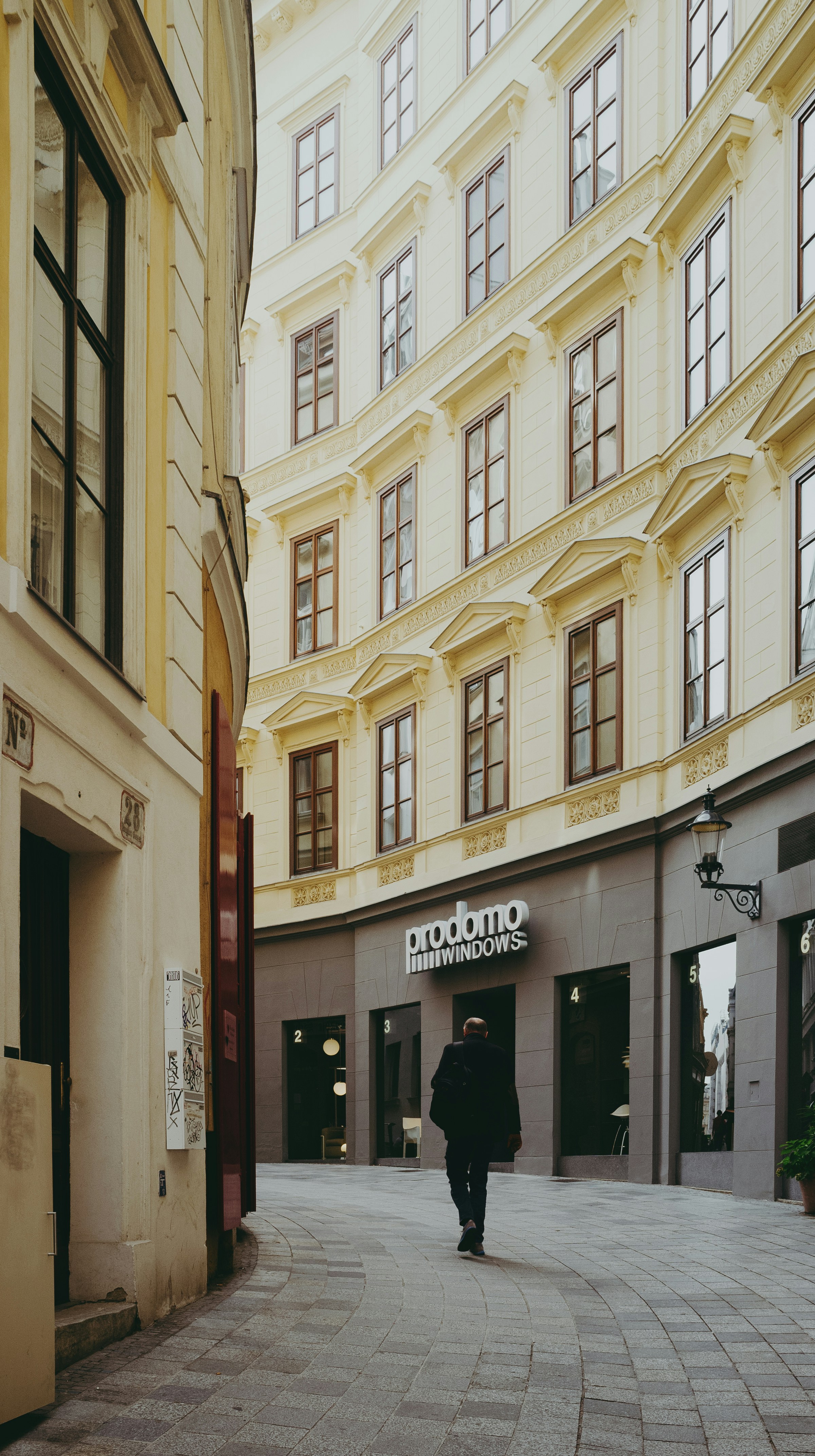 A solitary figure strolls through a charming, curved alleyway adorned with classic architecture and modern signage. The interplay of light and shadow enhances the scene's inviting atmosphere.