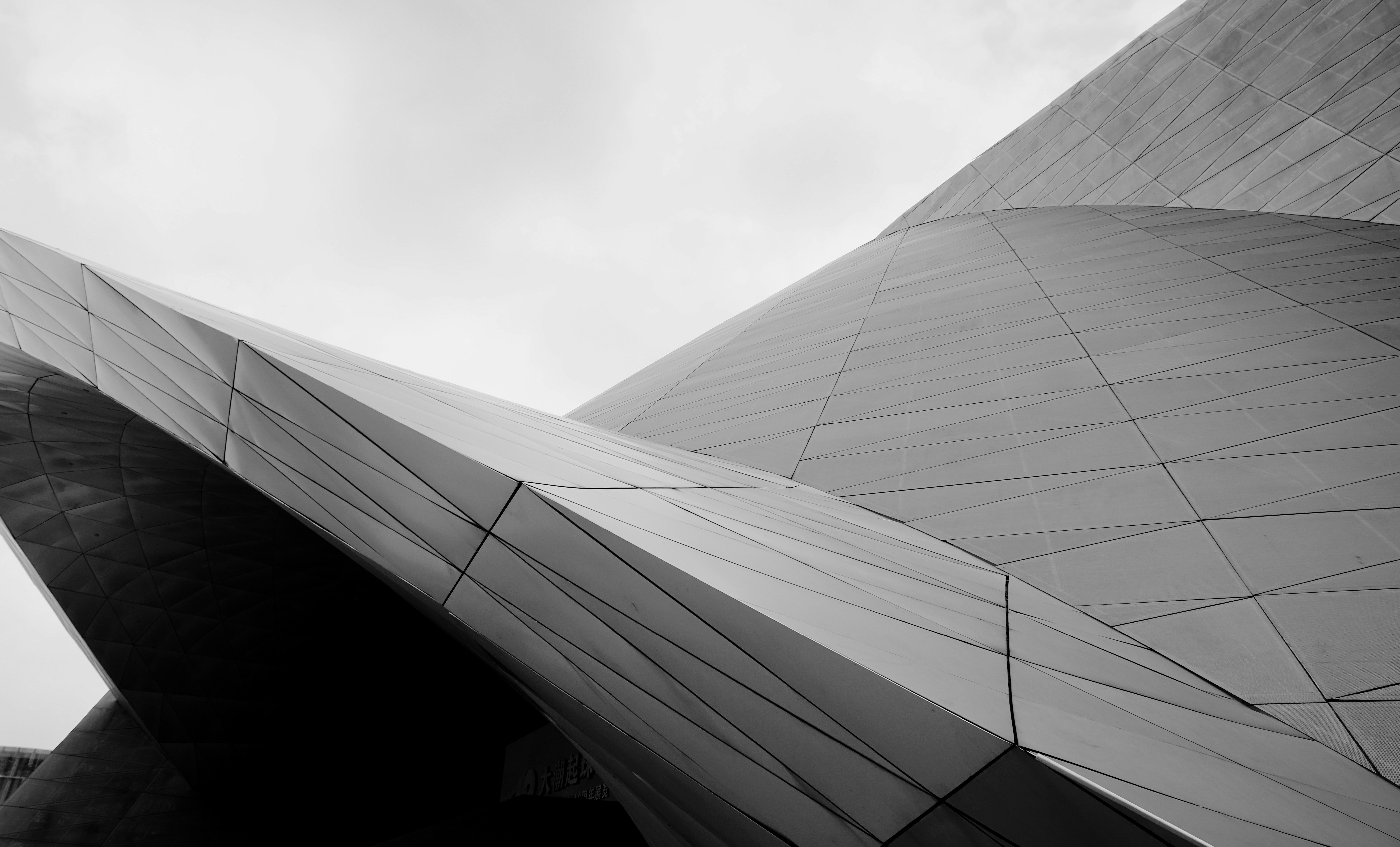 Dynamic architectural shapes converge under a cloudy sky, showcasing modern design. The interplay of angles and surfaces creates a striking visual narrative.