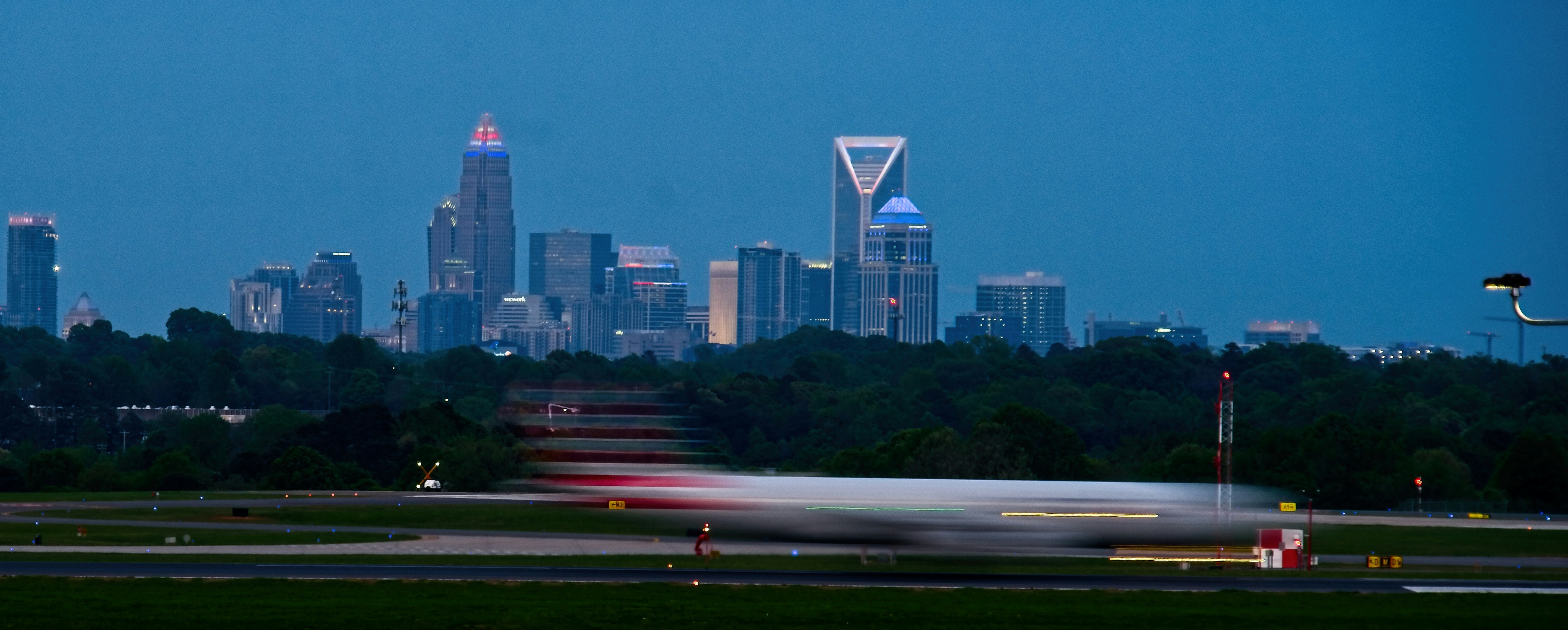 Airplane speeding along a runway at dusk with a city skyline glowing in the background.
