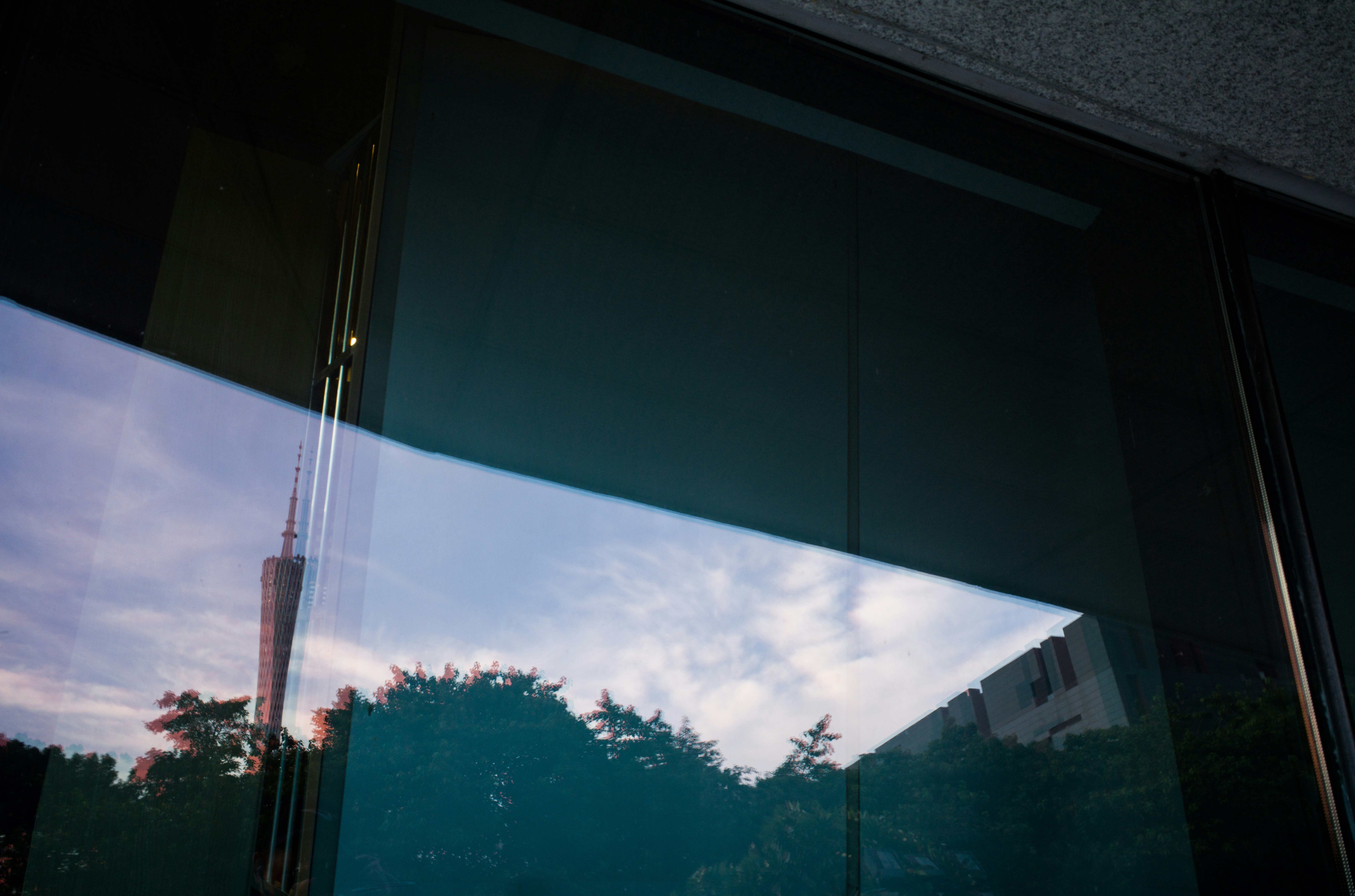 Skyline and trees reflected in a modern glass facade with soft evening light.