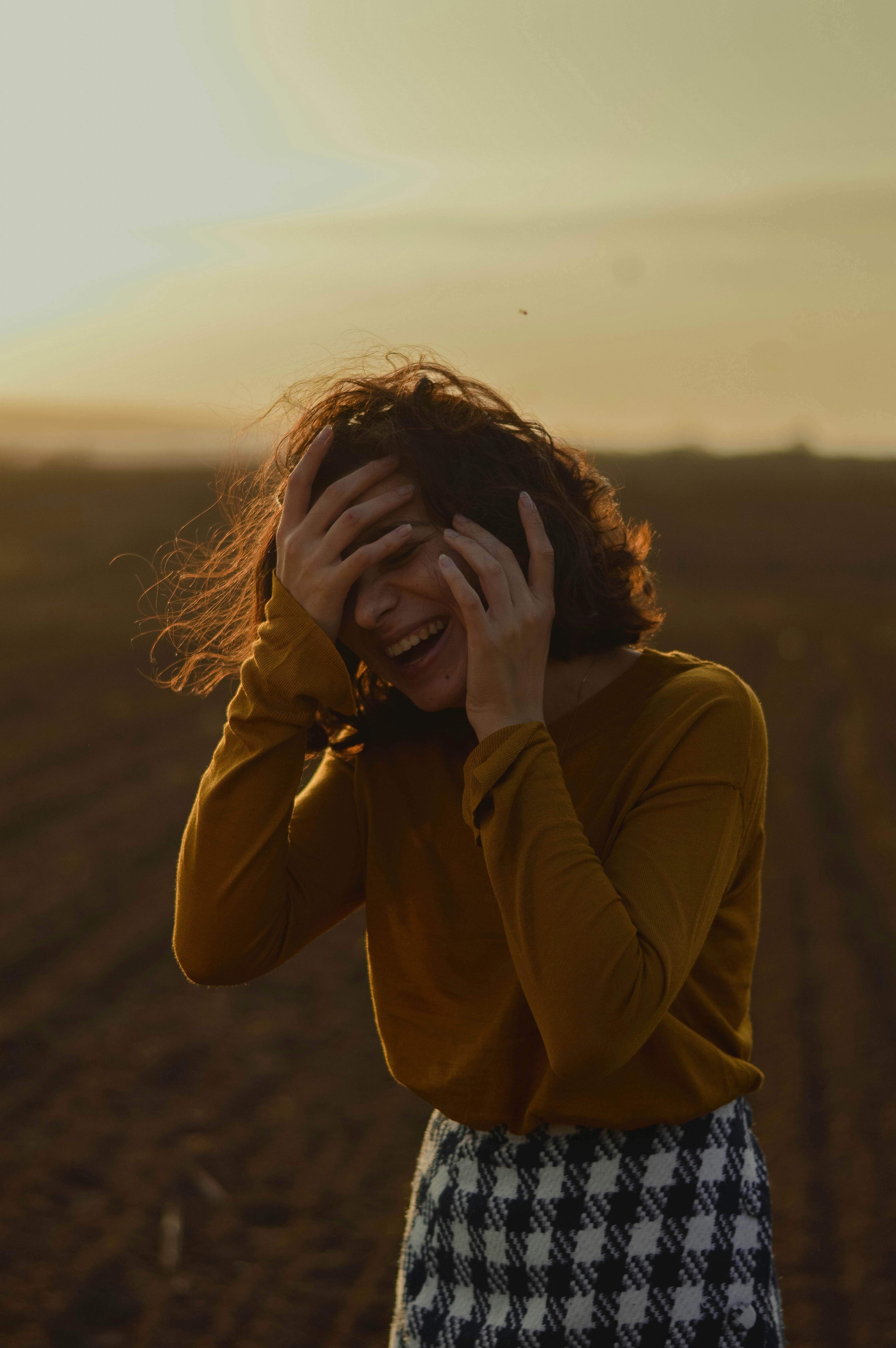 Golden Hour Joy: A Woman in a Field Laughs with Hands in Hair