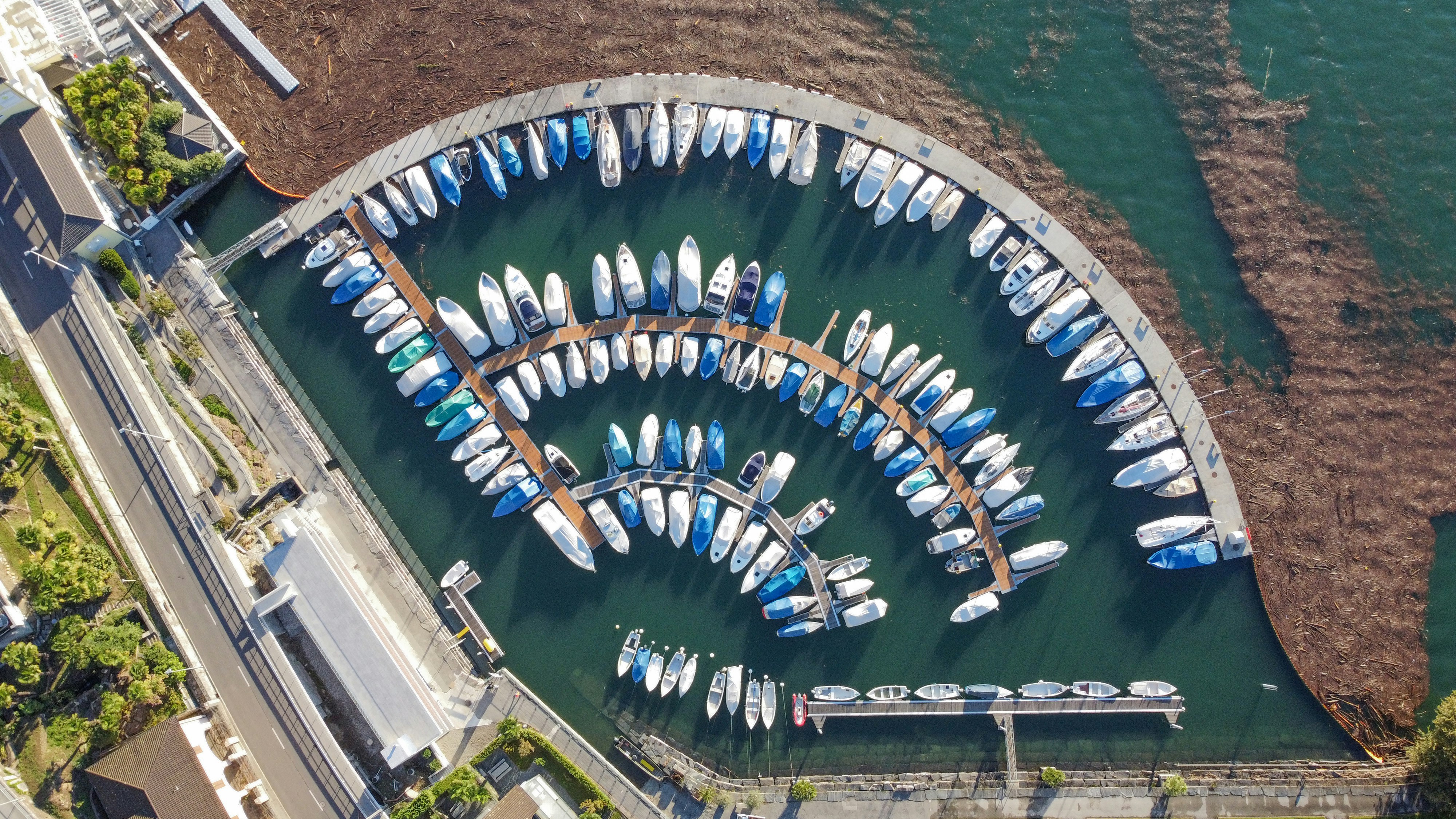 Aerial view of a marina featuring a circular arrangement of various boats, surrounded by vibrant water and lush greenery.