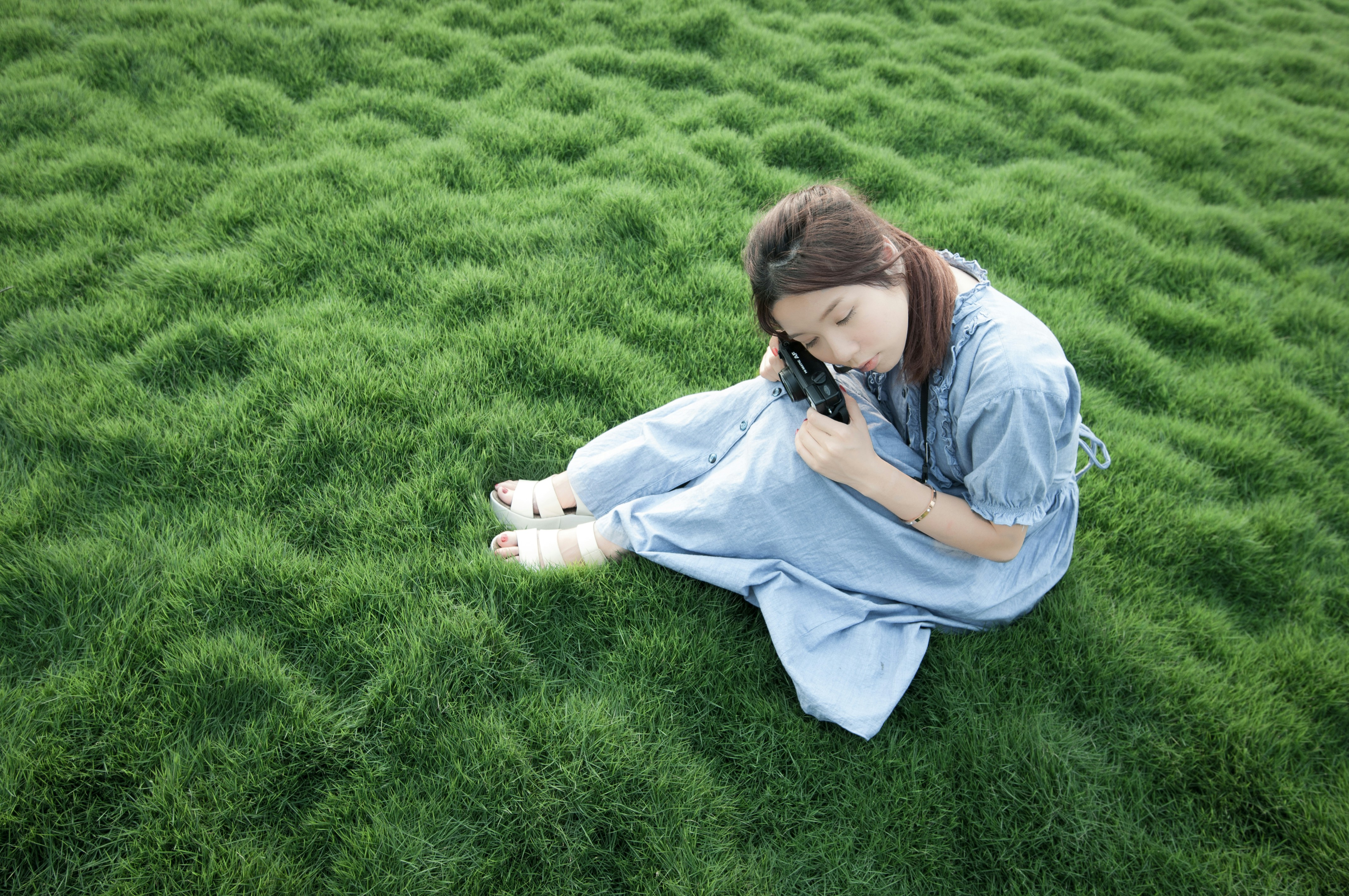 Grass Carpet Portrait: A Girl with a Camera Paused in Soft Light