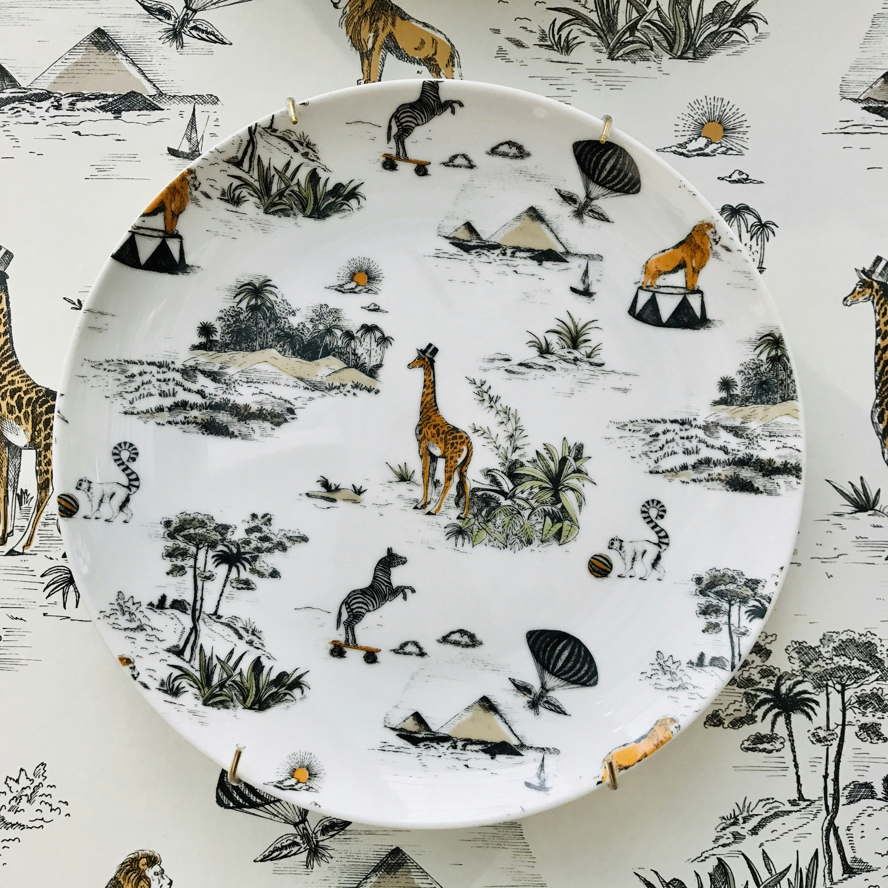 Decorative plate featuring a playful safari scene with giraffes, zebras, and mountains, set against a patterned background.