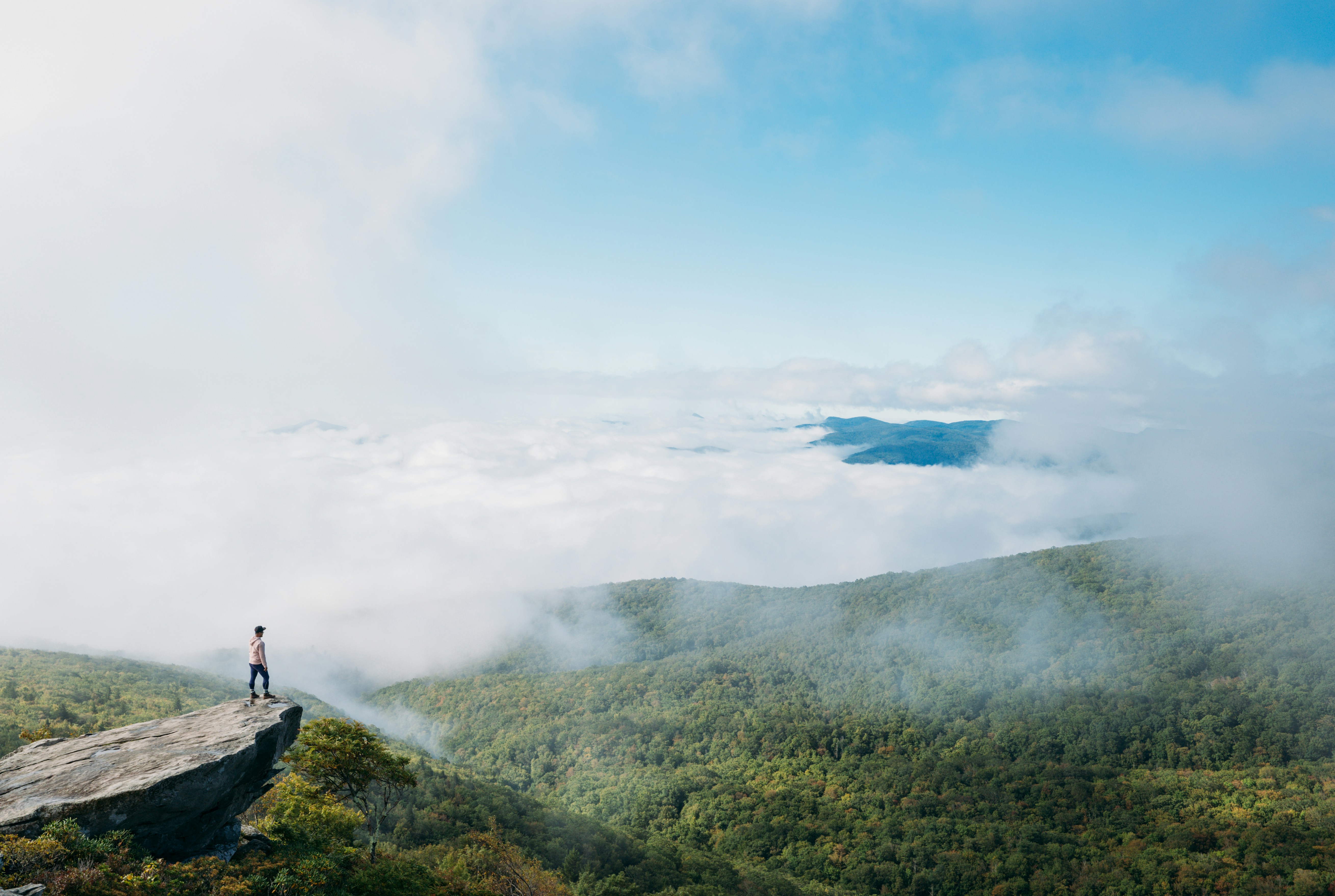 Person standing on rock near green grass field under white clouds ...