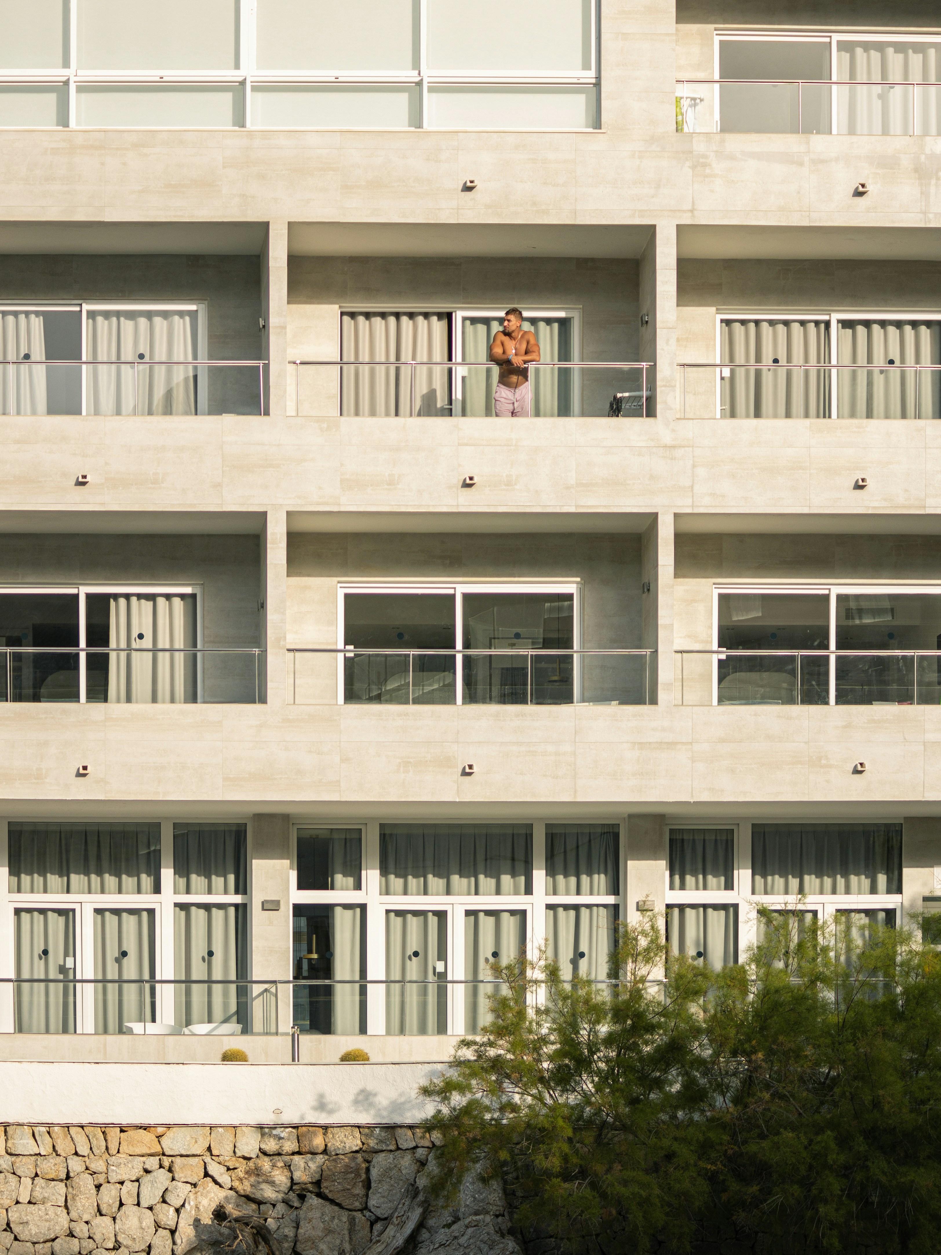 Person standing on a balcony of a modern apartment building in warm sunlight.