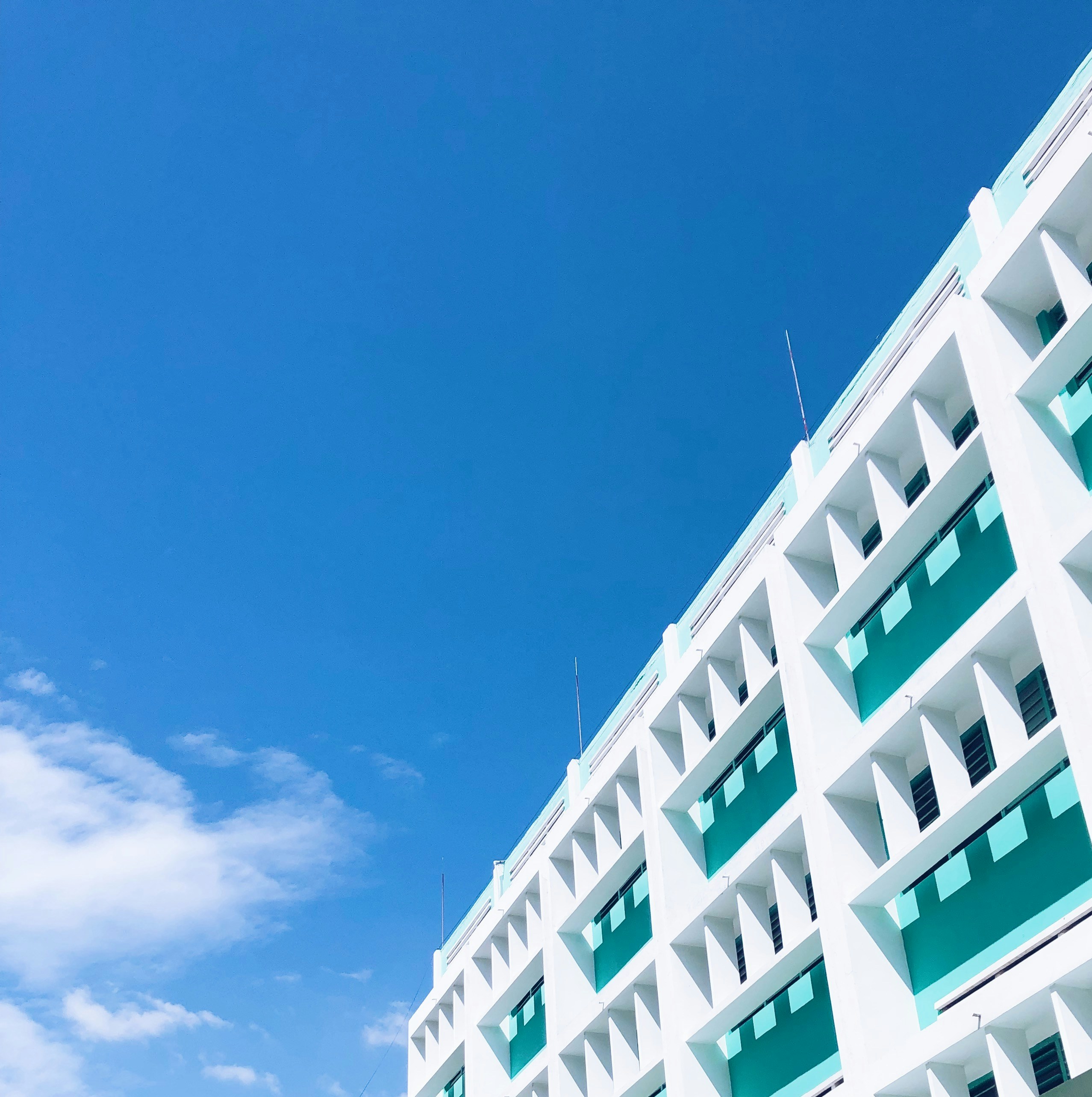 Modern building facade with turquoise accents against a vibrant blue sky, showcasing geometric design elements and sunlight reflections.