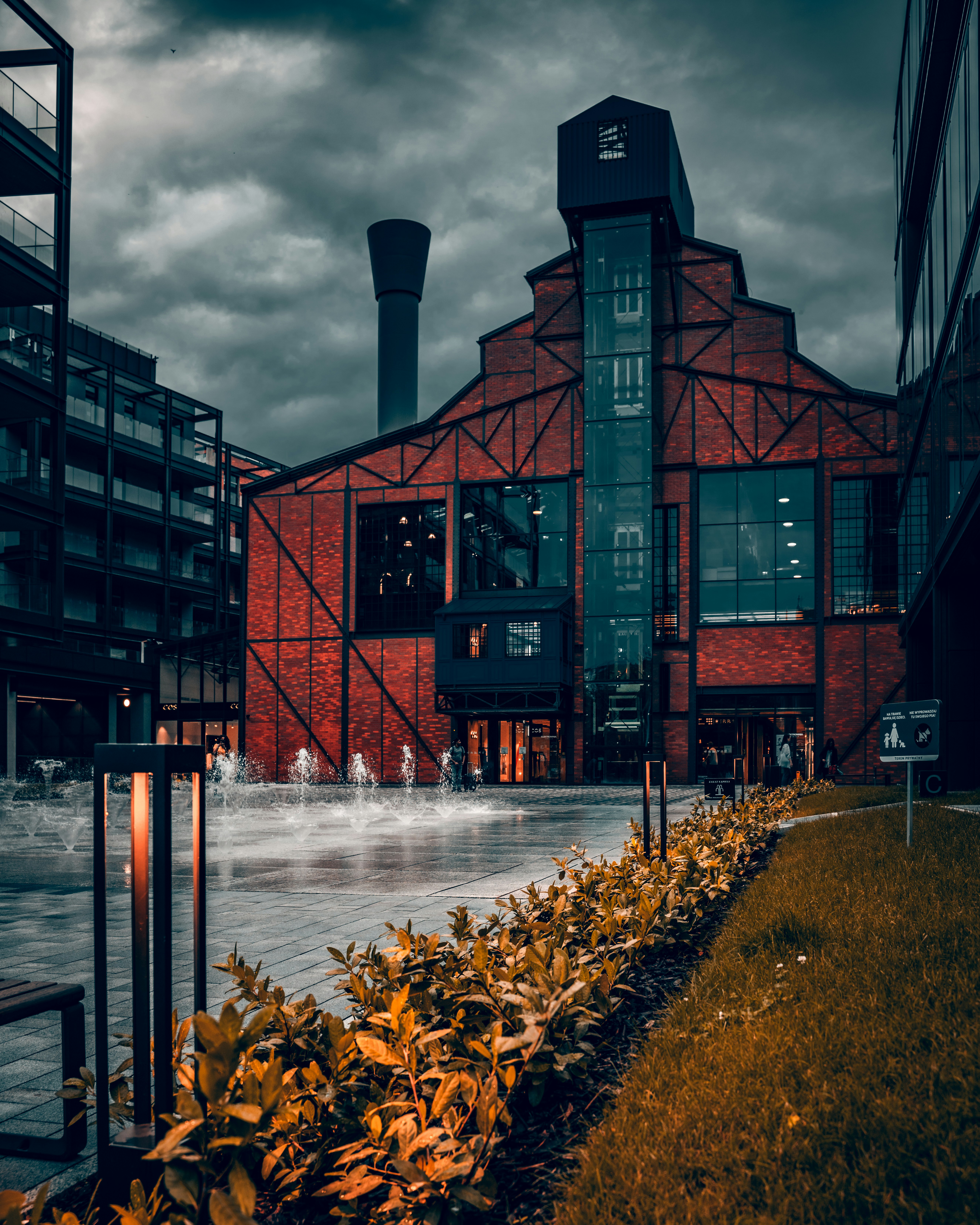 Refurbished power plant building transformed into a modern shopping mall with vibrant red brick facade and glass elements.