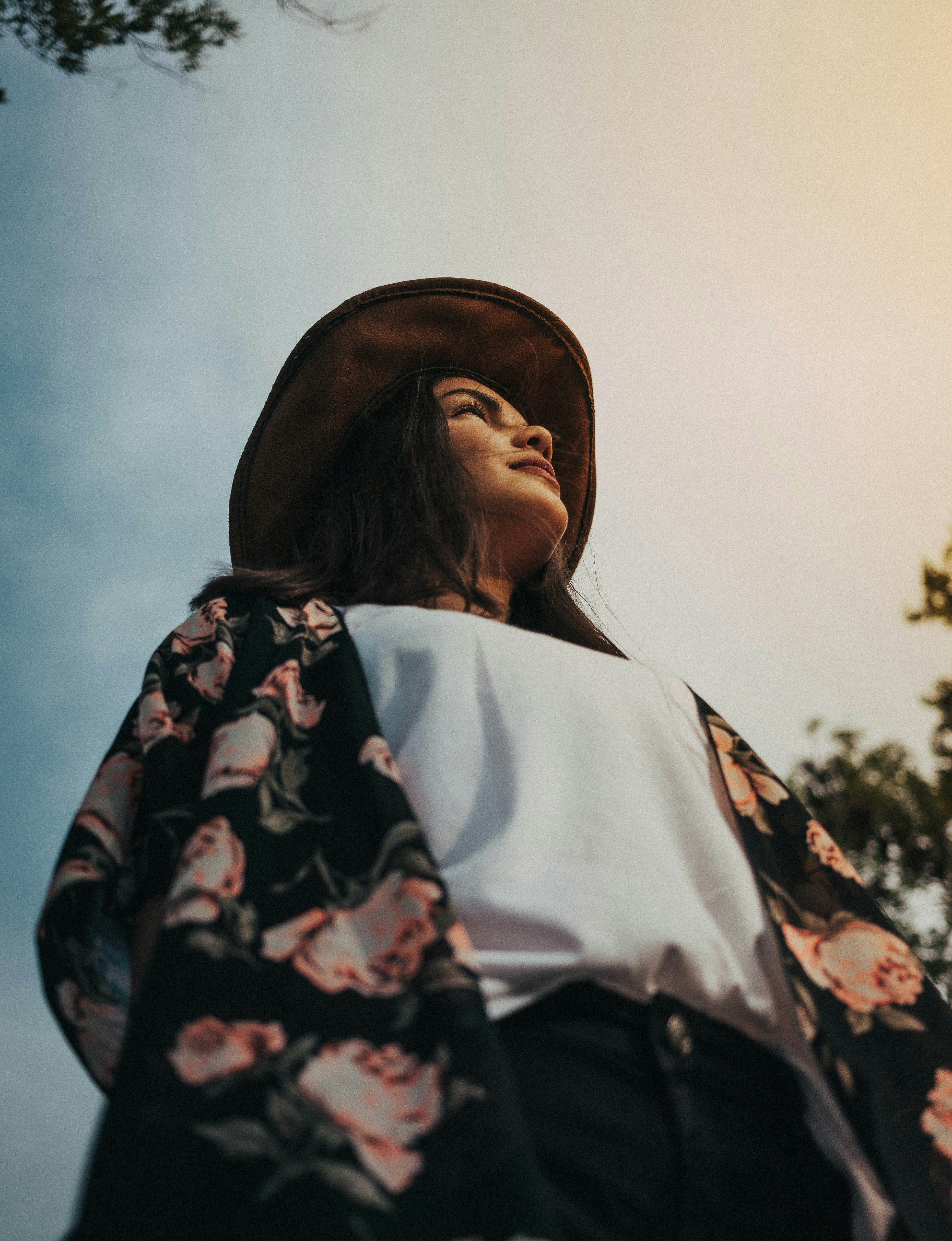 A woman in a floral kimono and hat gazes upward, framed by a clear sky and soft sunlight, embodying a sense of hope and tranquility.