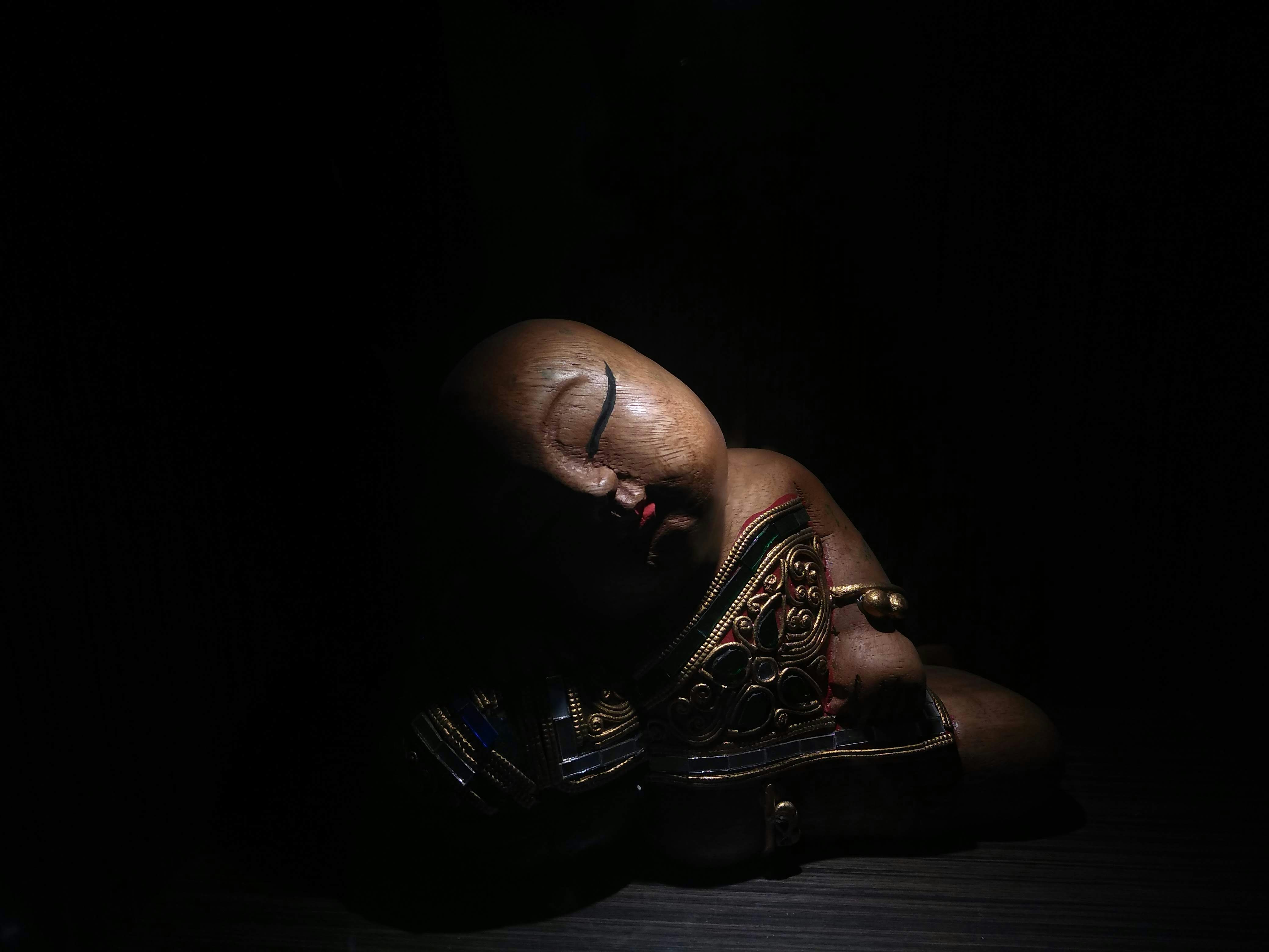 Carved wooden figure of a serene child resting peacefully, illuminated by a soft light against a dark background.