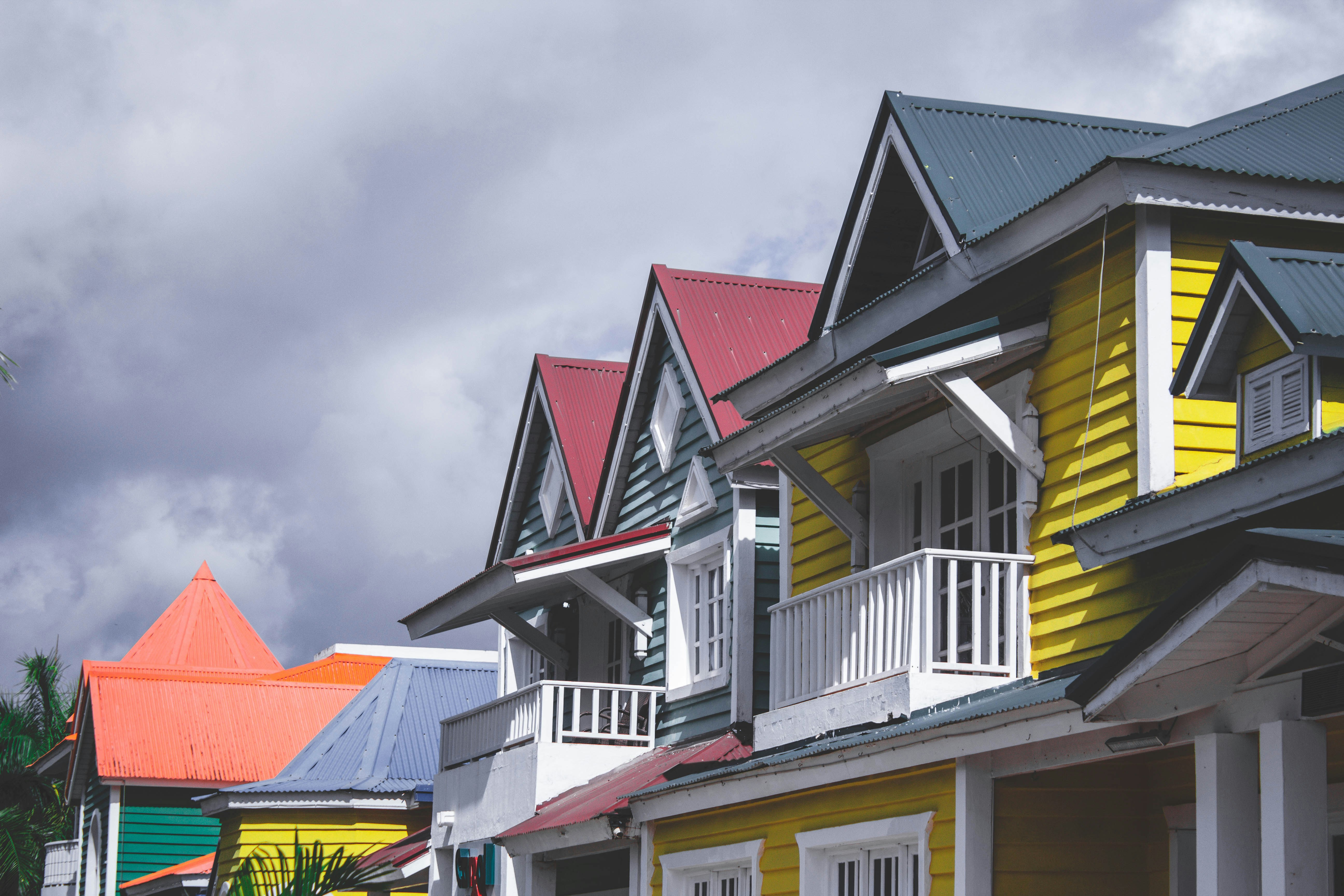 Colorful houses with distinct roofs in a vibrant neighborhood, showcasing local architectural styles against a cloudy sky.
