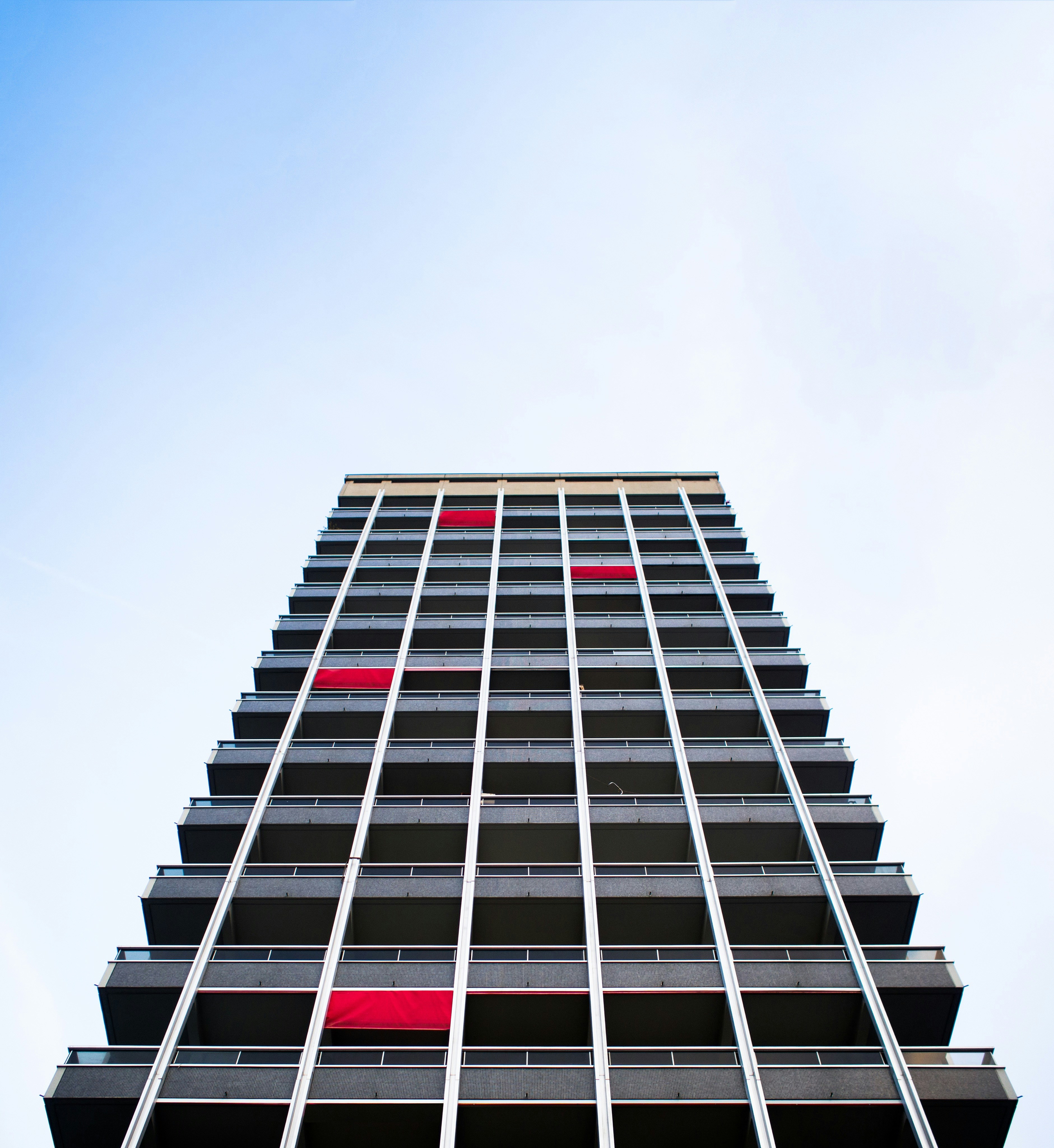 Modern high-rise building showcasing a grid of balconies with vibrant red accents against a clear blue sky.