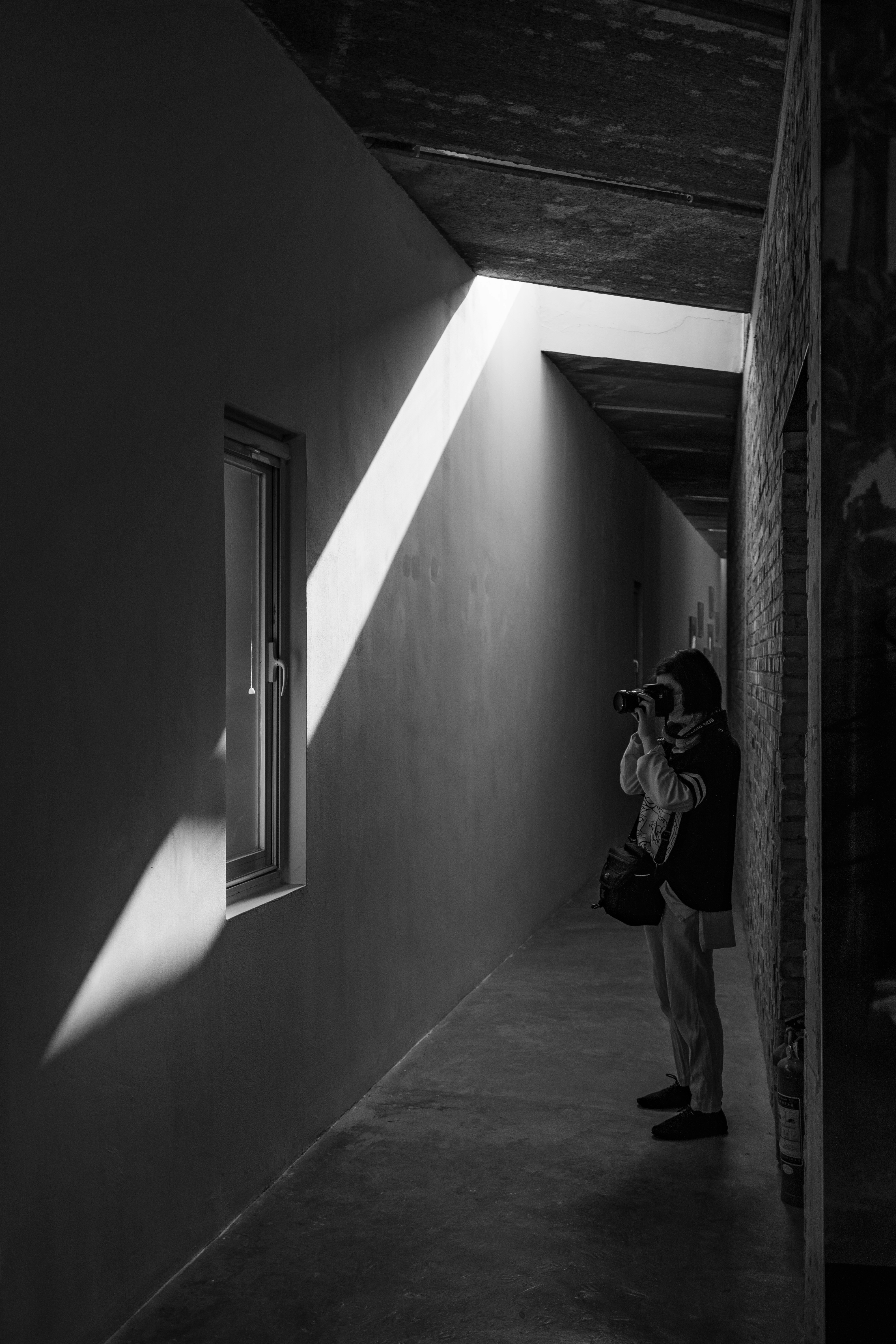 A photographer captures the interplay of light and shadow in a narrow corridor, framed by a window's beam. The scene is rendered in striking black and white.