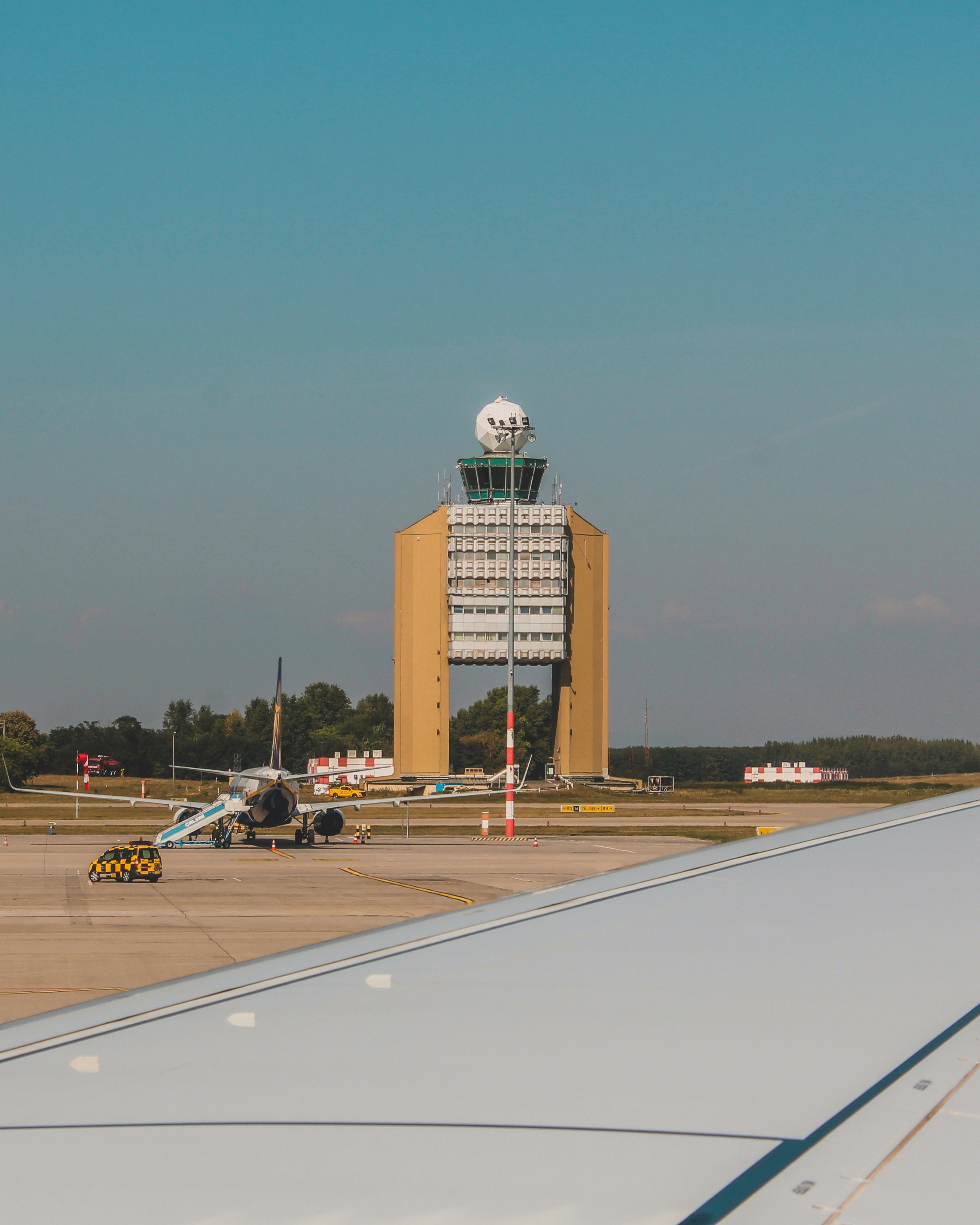 Airport control tower with a radar dome, airplane, and tarmac in foreground under clear blue sky.