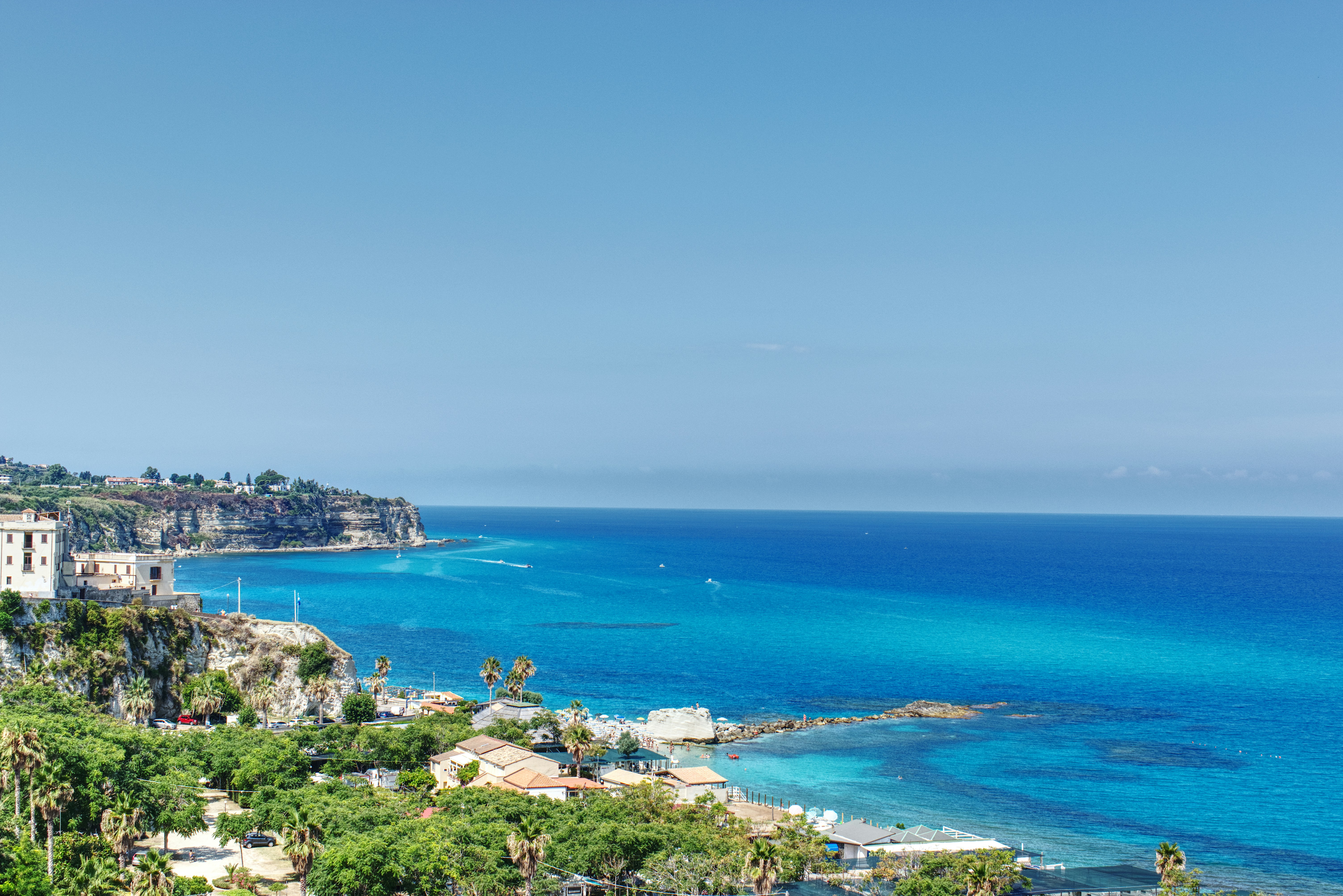 Vivid turquoise waters stretch along the rocky coastline of Tropea under a clear blue sky.