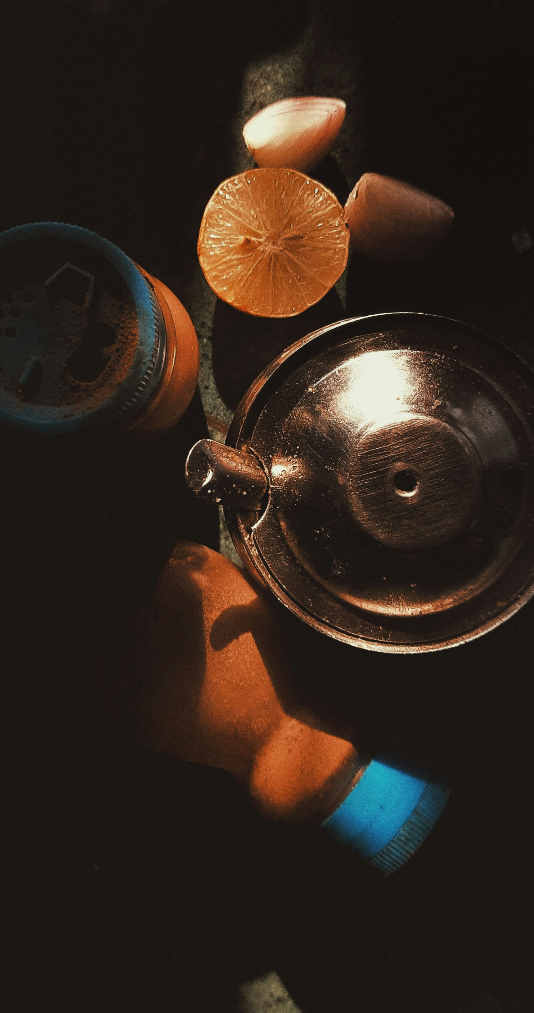A vibrant still life featuring a halved lemon, garlic cloves, and a metallic container, highlighting the interplay of light and shadow.