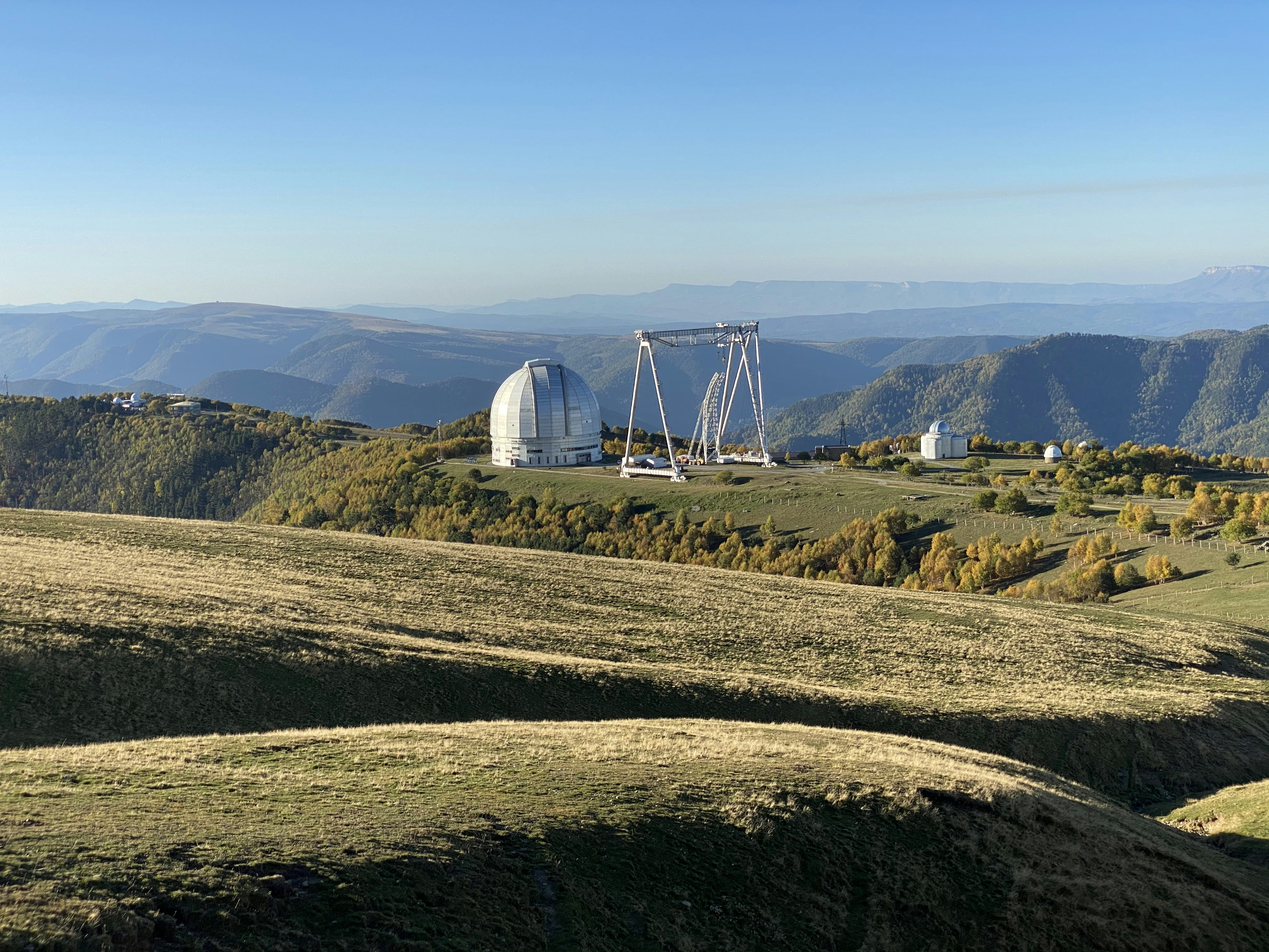 Observatory structures nestled in a mountainous landscape, surrounded by rolling hills and autumn foliage.