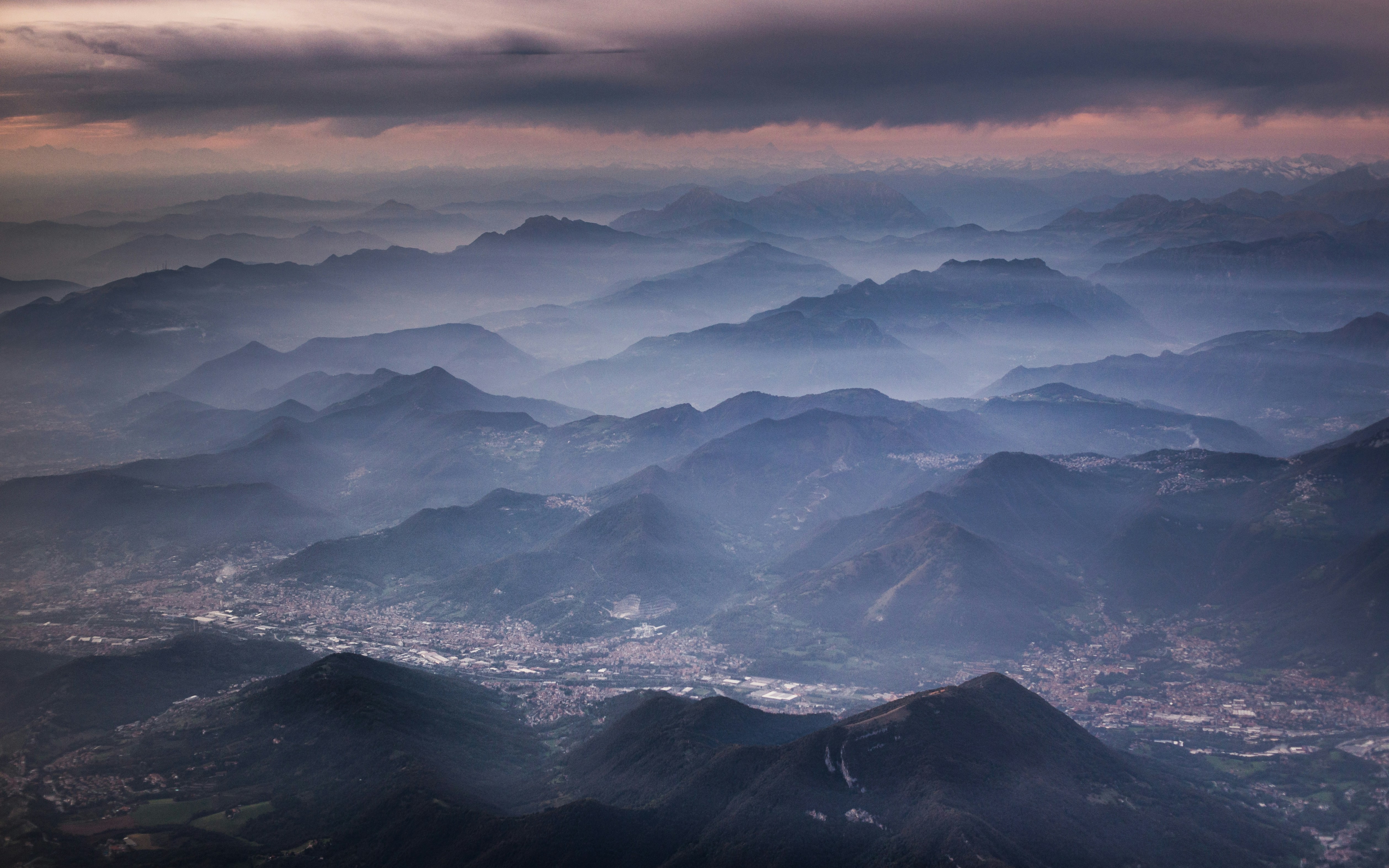 Fog drapes over layered mountain ranges at twilight, creating a serene, mystical atmosphere.