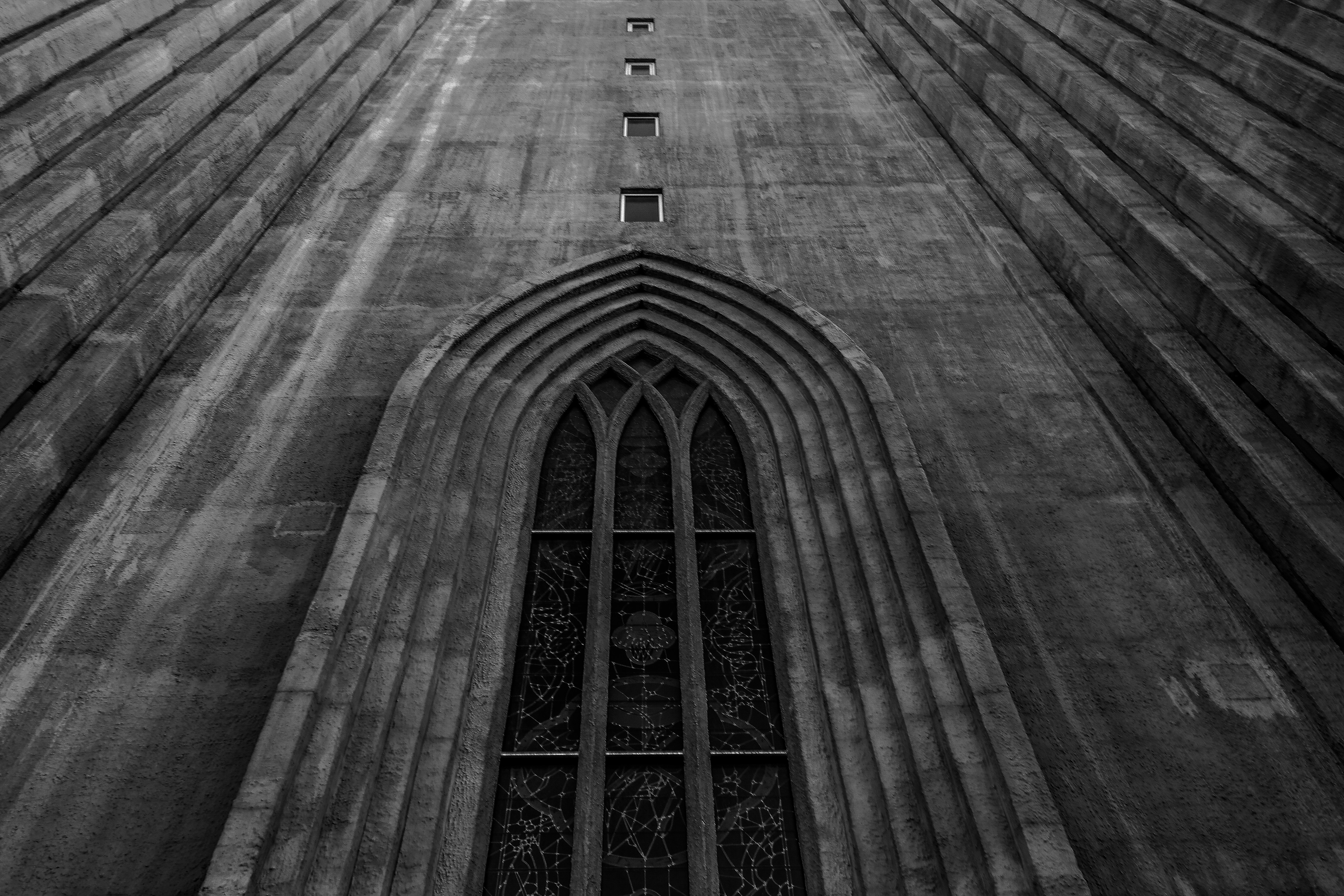 Gothic-style window framed by textured stone walls, viewed from a low angle, highlighting architectural details and symmetry.