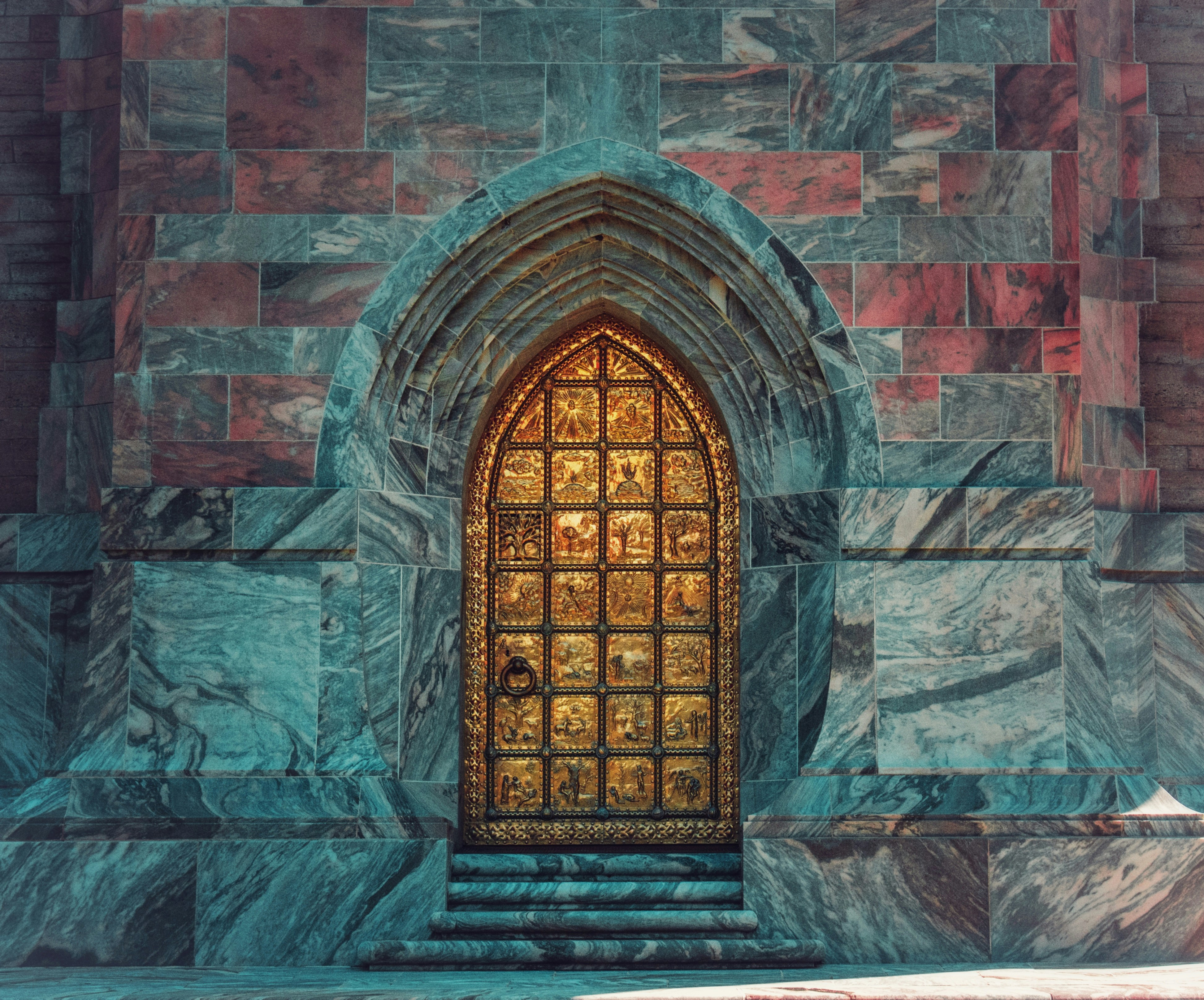 Intricately designed golden door set against a backdrop of colorful stone masonry. The ornate details highlight craftsmanship and architectural beauty.