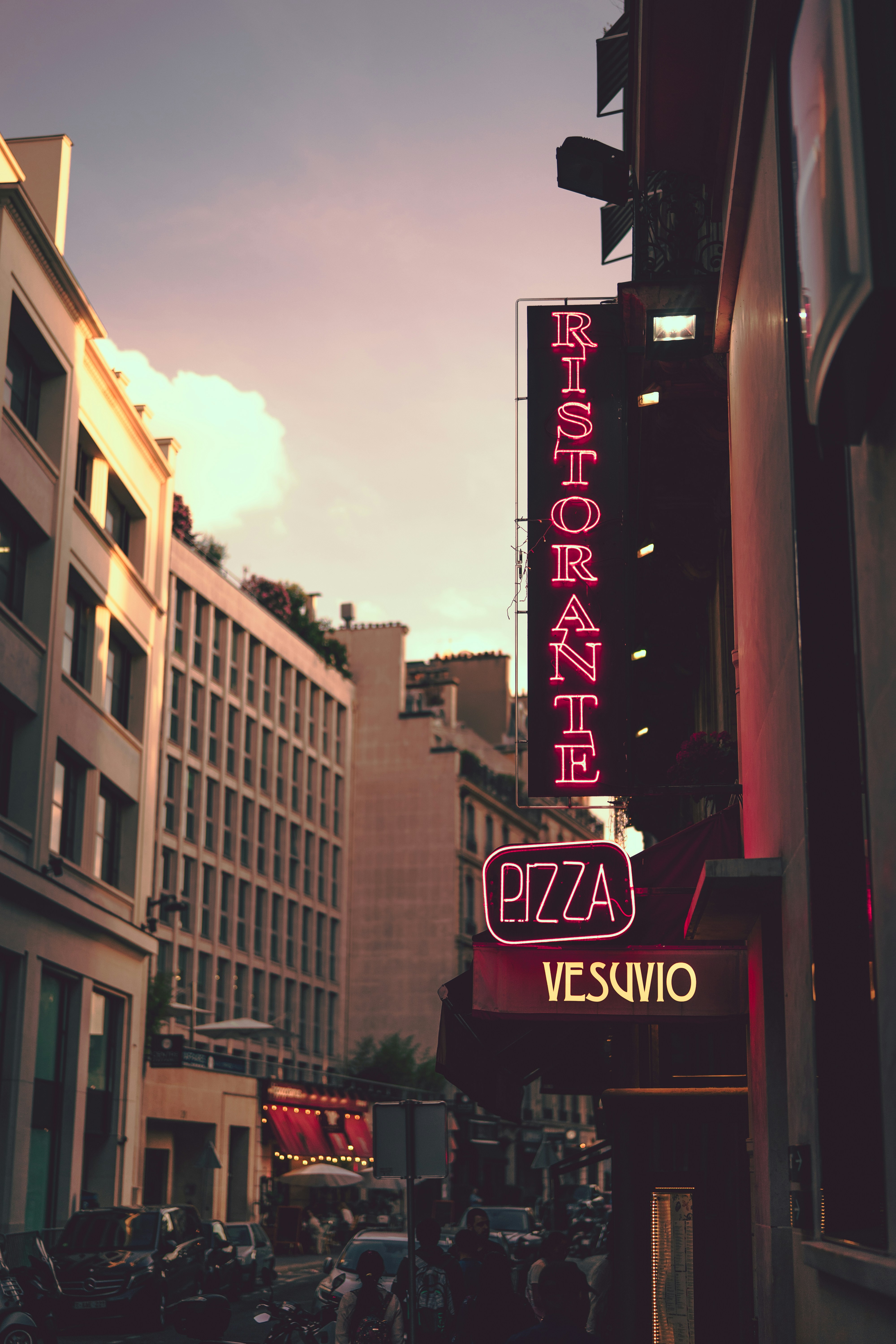 Vibrant neon signs illuminate a narrow street lined with buildings, showcasing a charming Italian restaurant atmosphere.