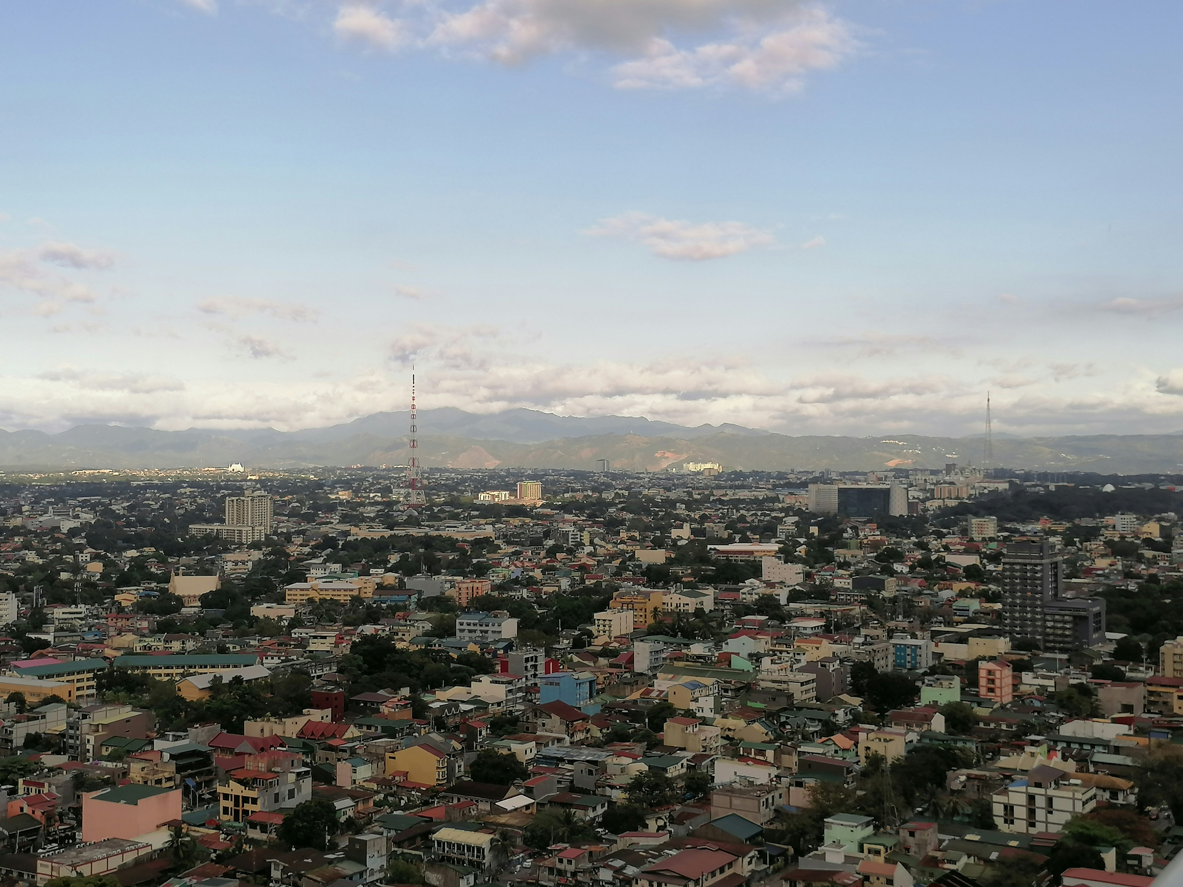Vast cityscape showcasing a blend of residential and commercial buildings under a pastel sky, with distant mountains framing the horizon.