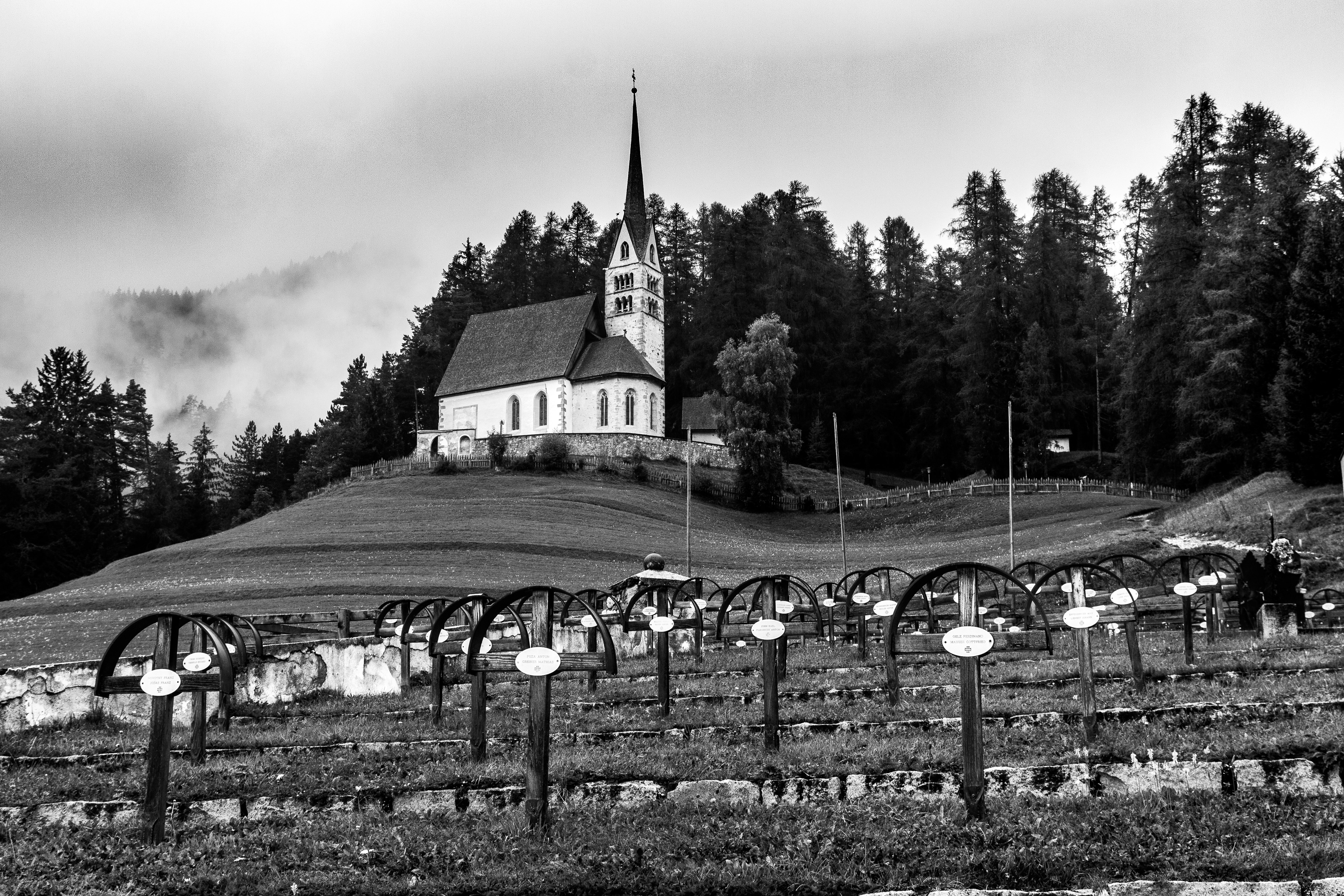 WWI cemetery with the medieval church of Saint Uliana on a hill, surrounded by dense forest.